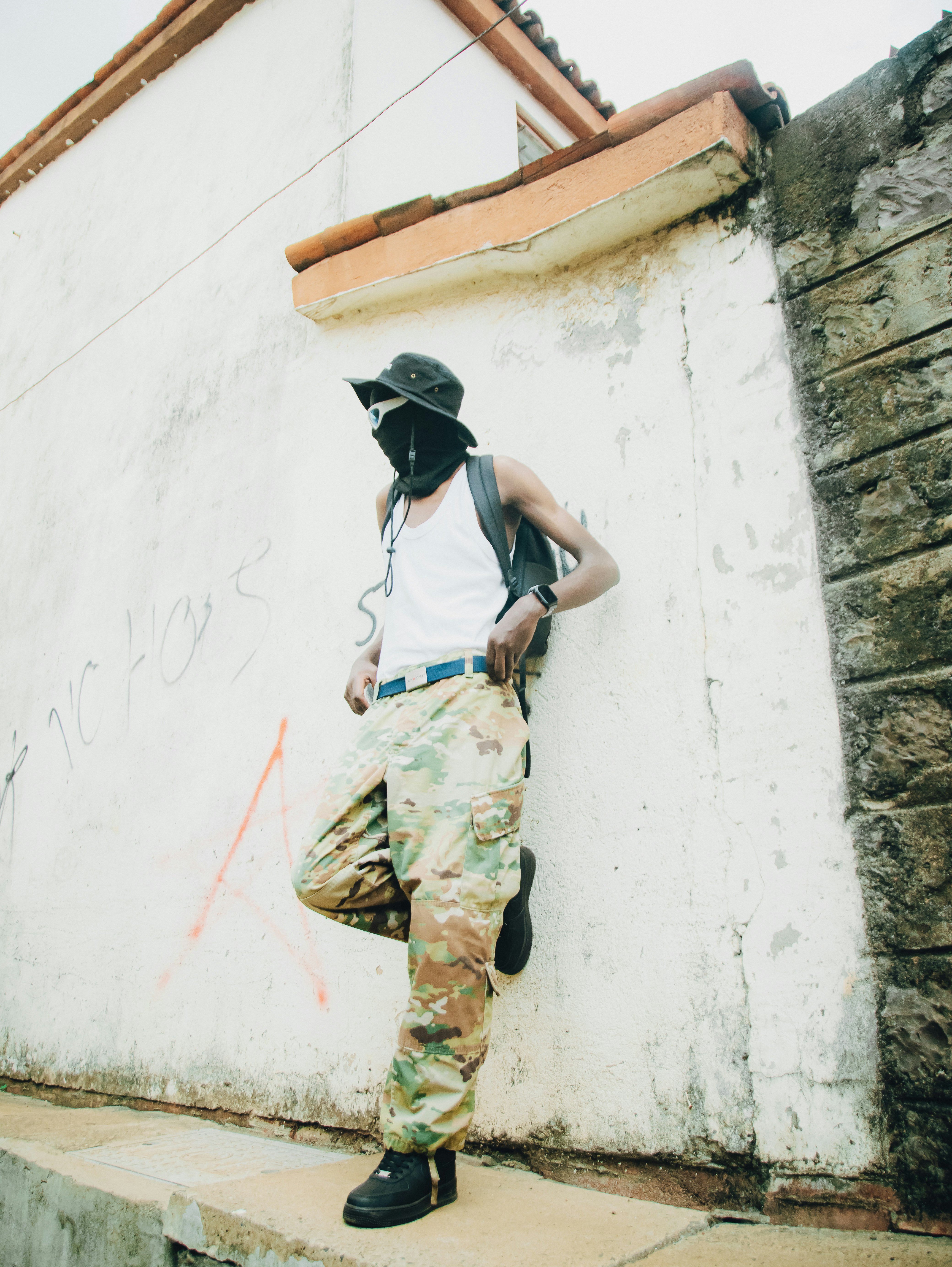 Masked wanderer in camouflage against a sunlit wall