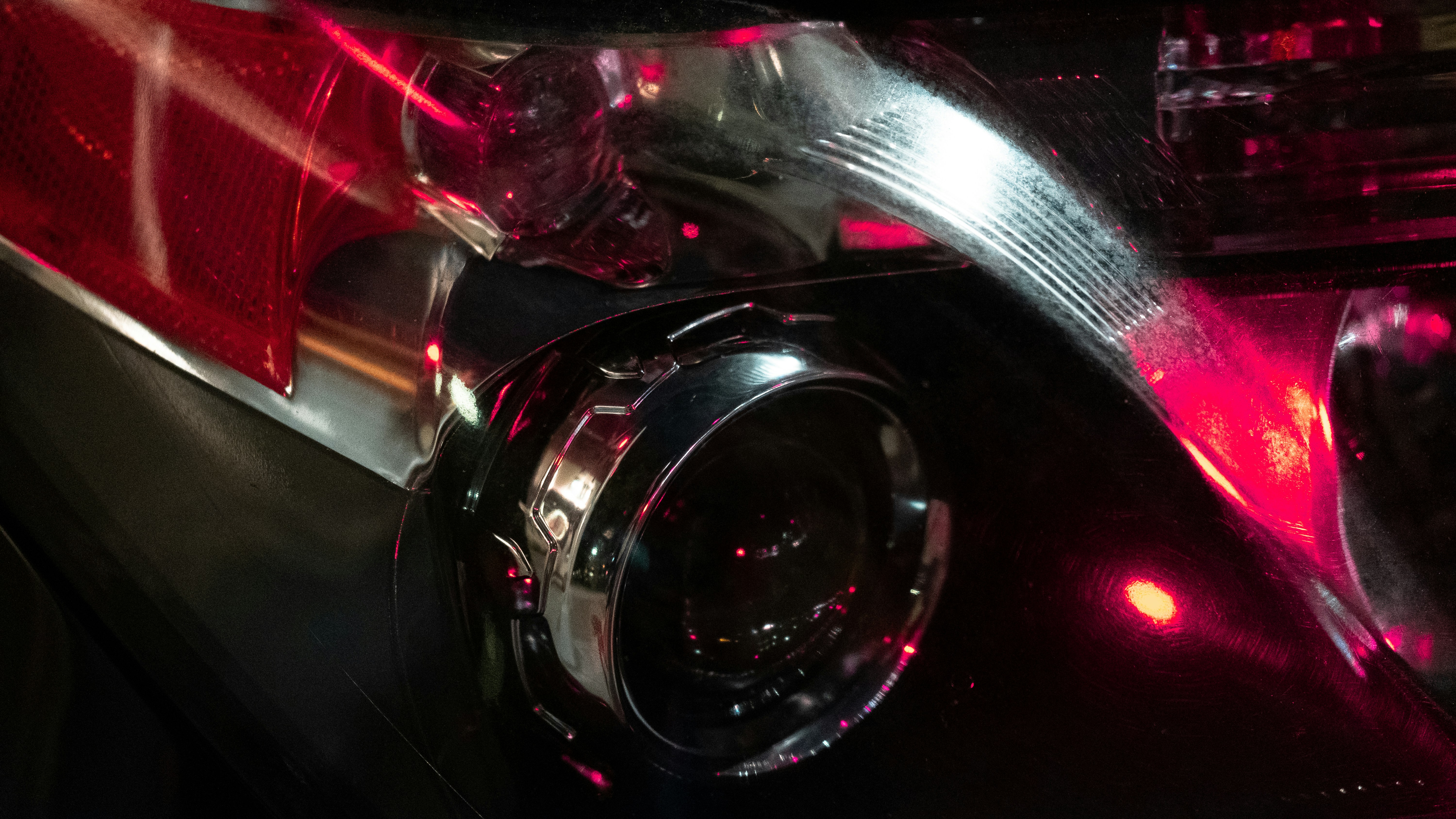 Chromed Lens and Neon Gleam: Night-time Car Headlight Under Red Sky