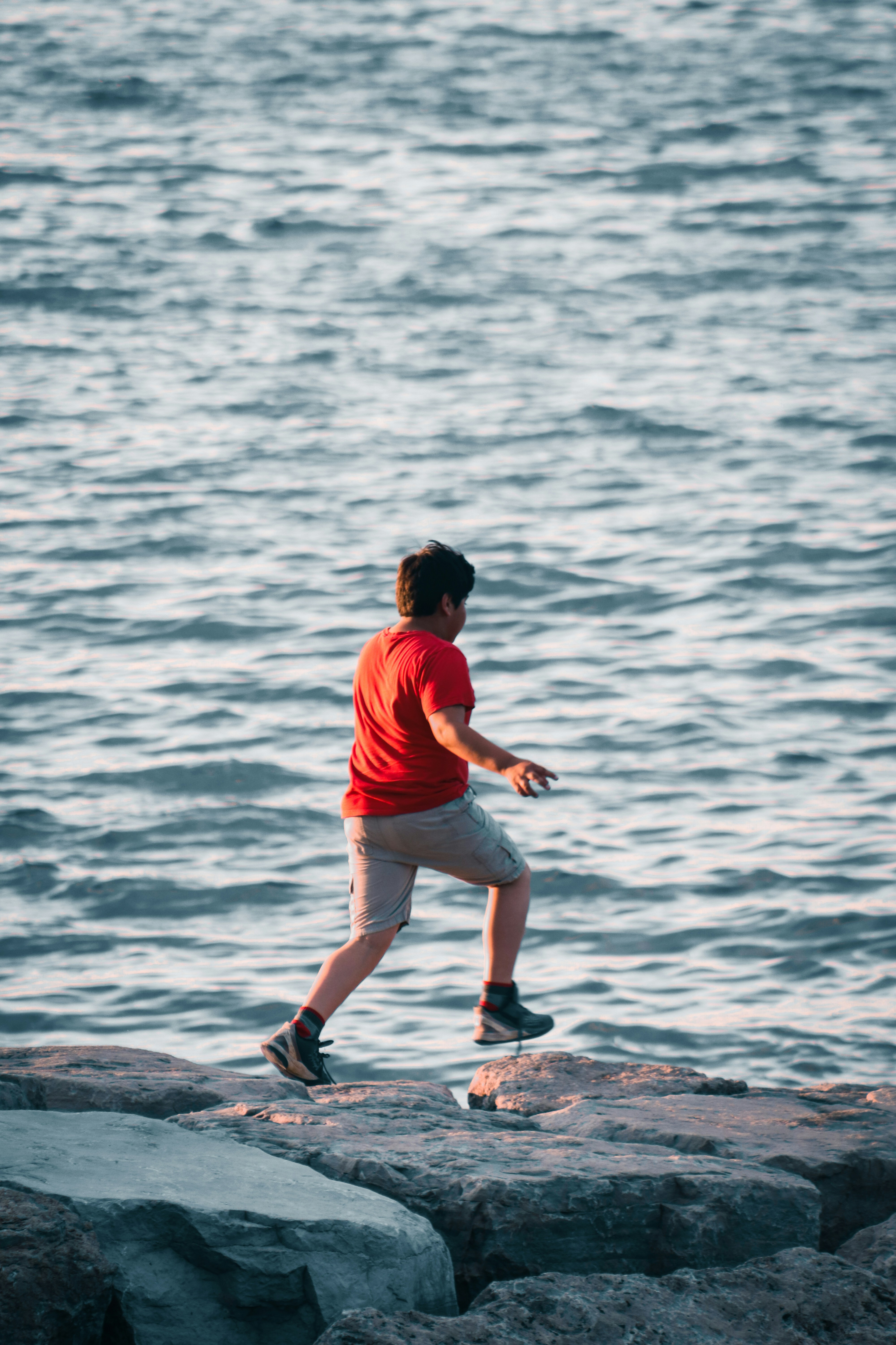 Red-clad climber stepping onto rocky shoreline by the sea