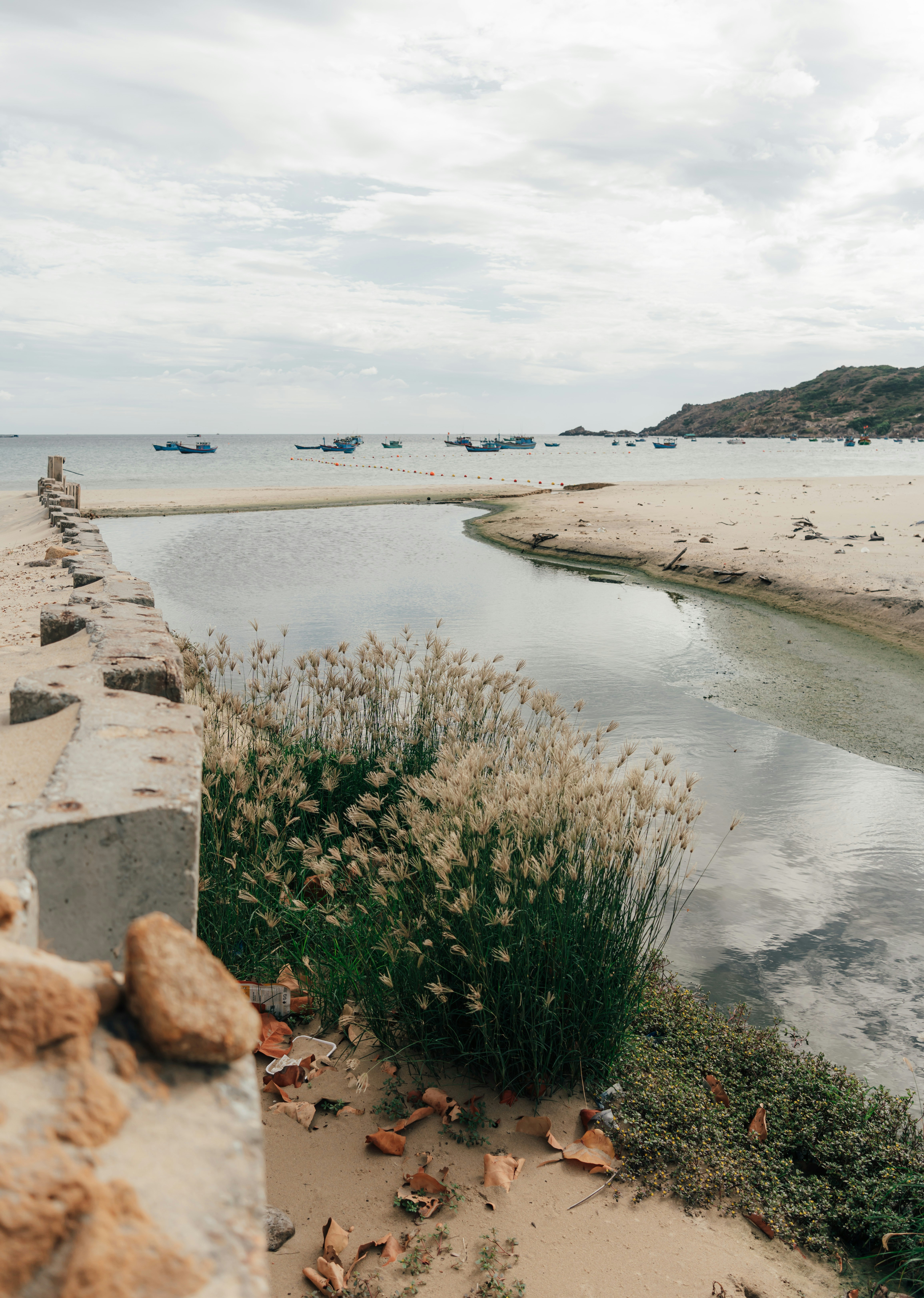 Coastal Creek: Stones, Grass, and Boats Beneath a Quiet Sky
