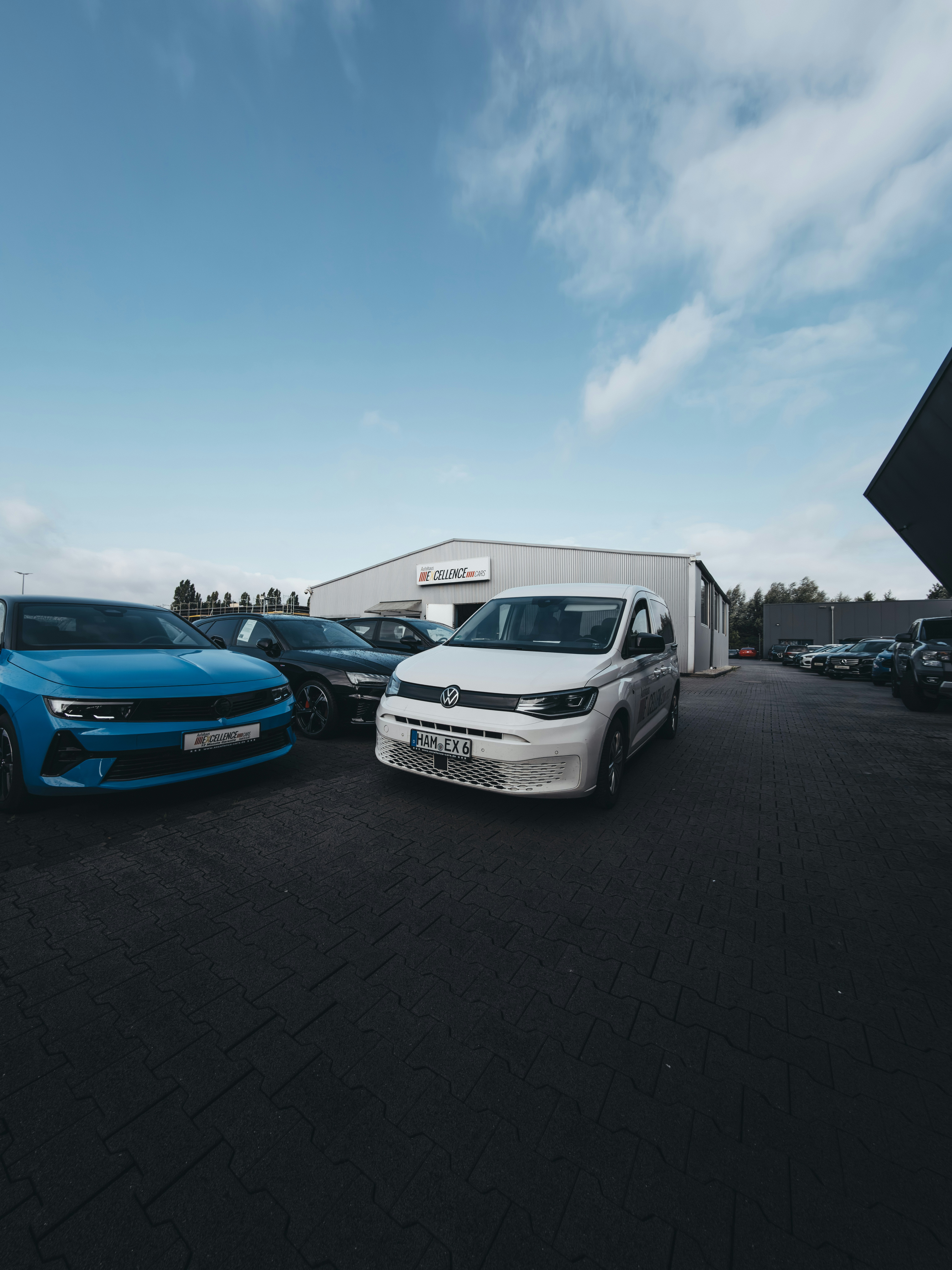 White van at the center of a car lot under a blue sky