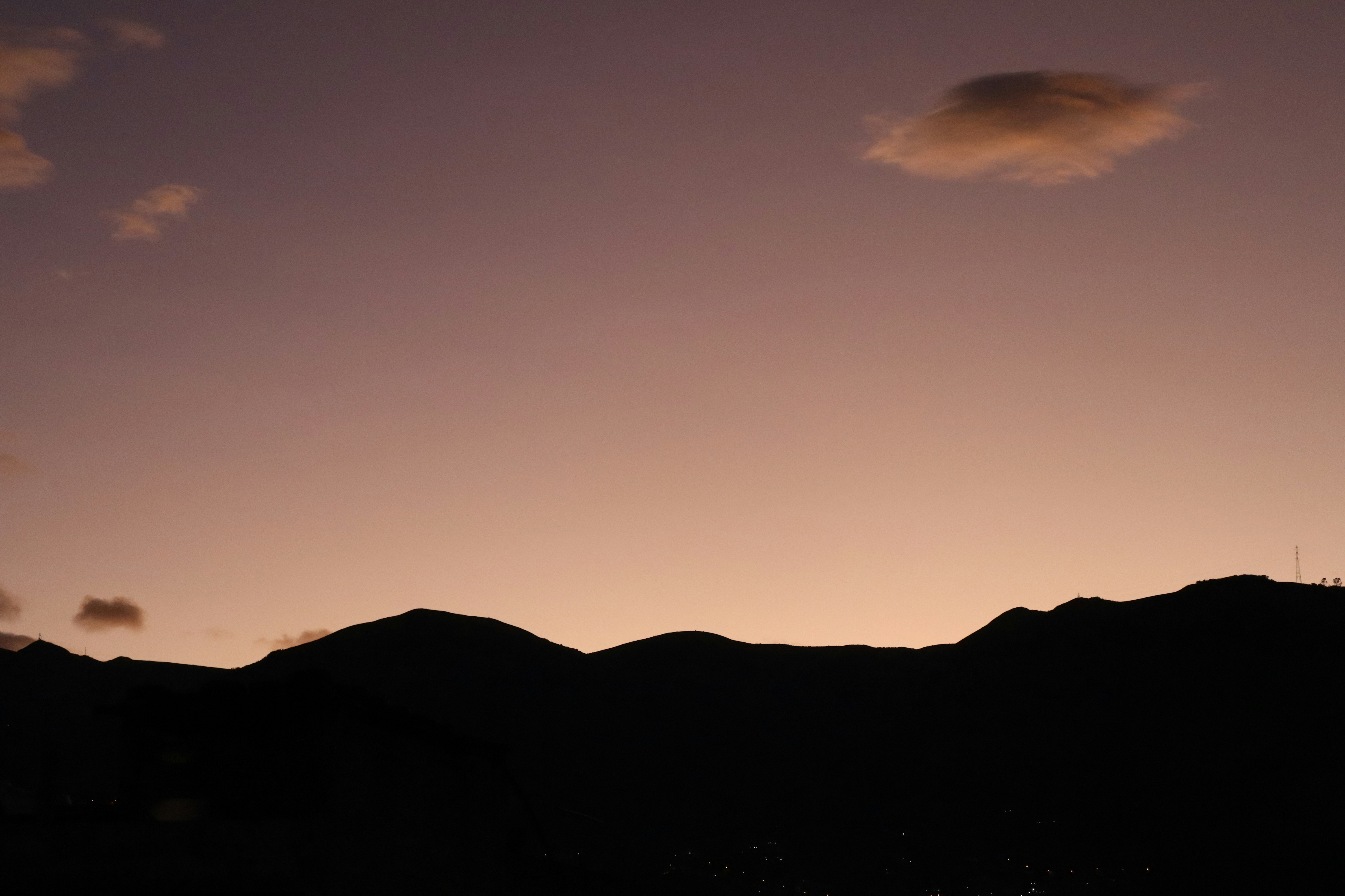 Dusk silhouettes of distant hills against a pastel sky; a tranquil landscape captured at twilight, with a subtle hint of distant lights along the valley.