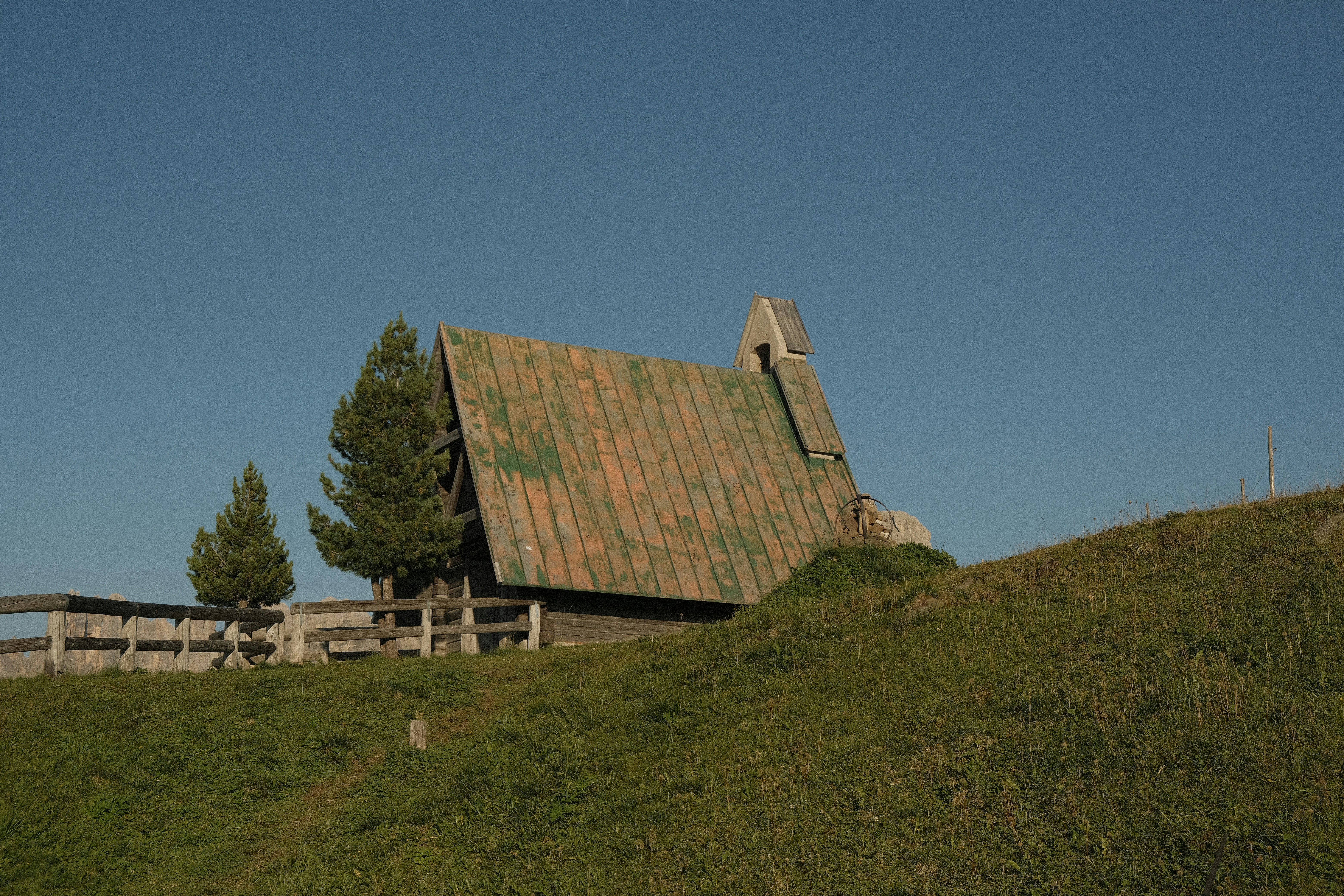A rustic hillside chapel tilts toward the horizon beneath a clear blue sky