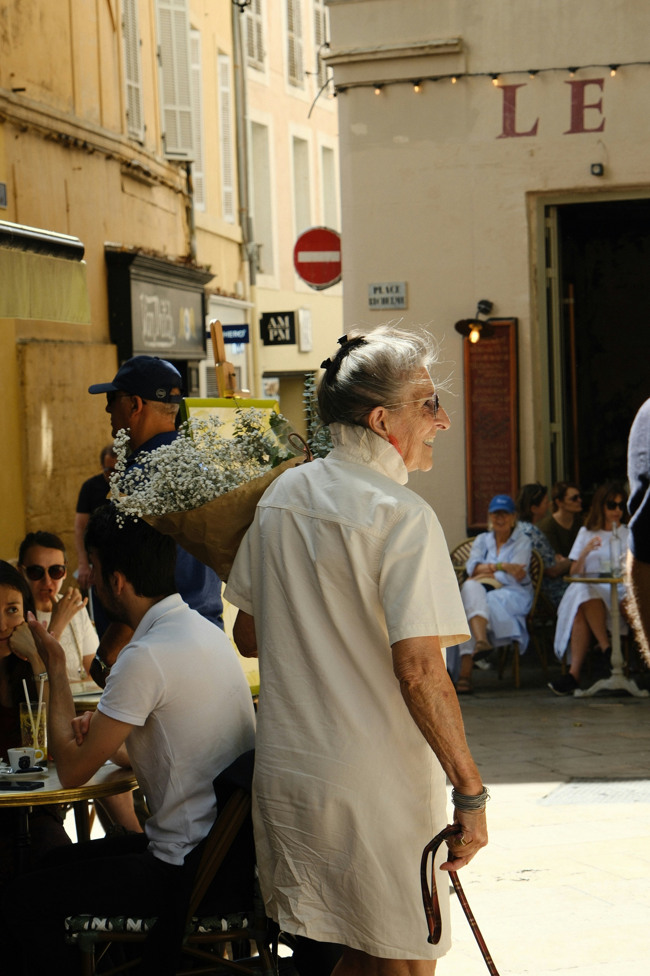The Street Portrait: Elderly Woman with Cane in Sunlit Café Quarter