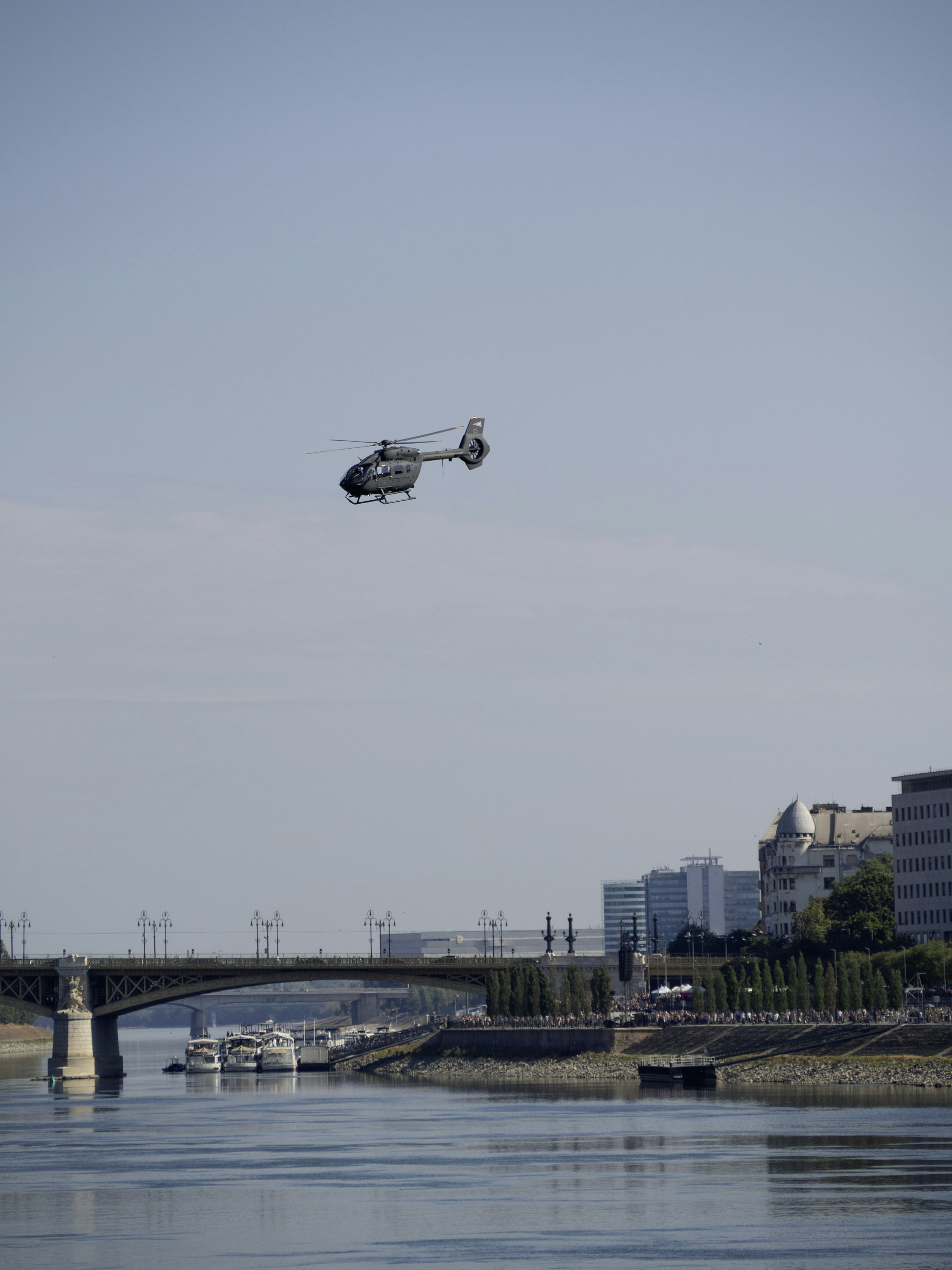 A lone helicopter glides above a sunlit city river