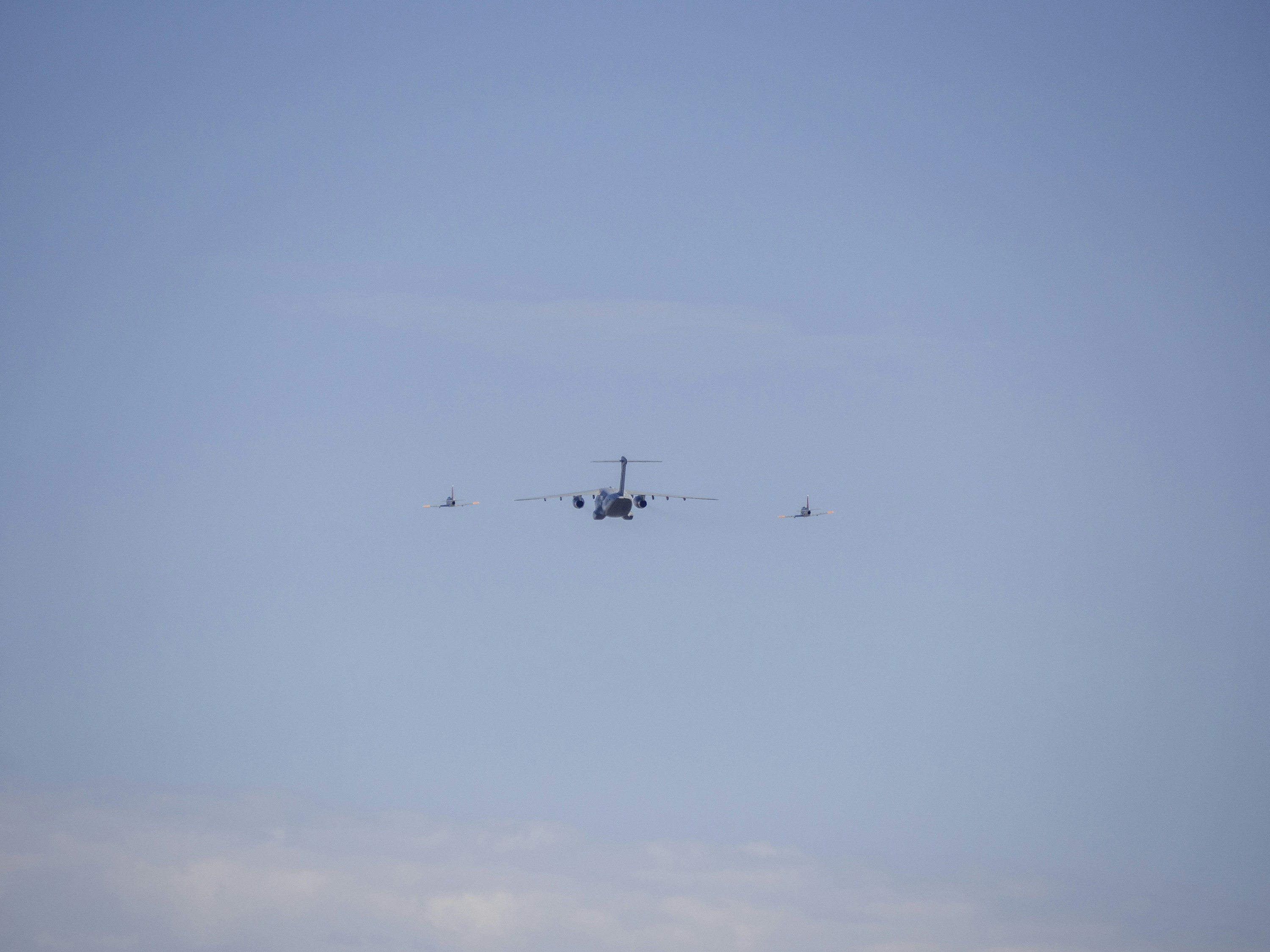 Midair Arrival: A distant military aircraft punctuating a pale blue horizon