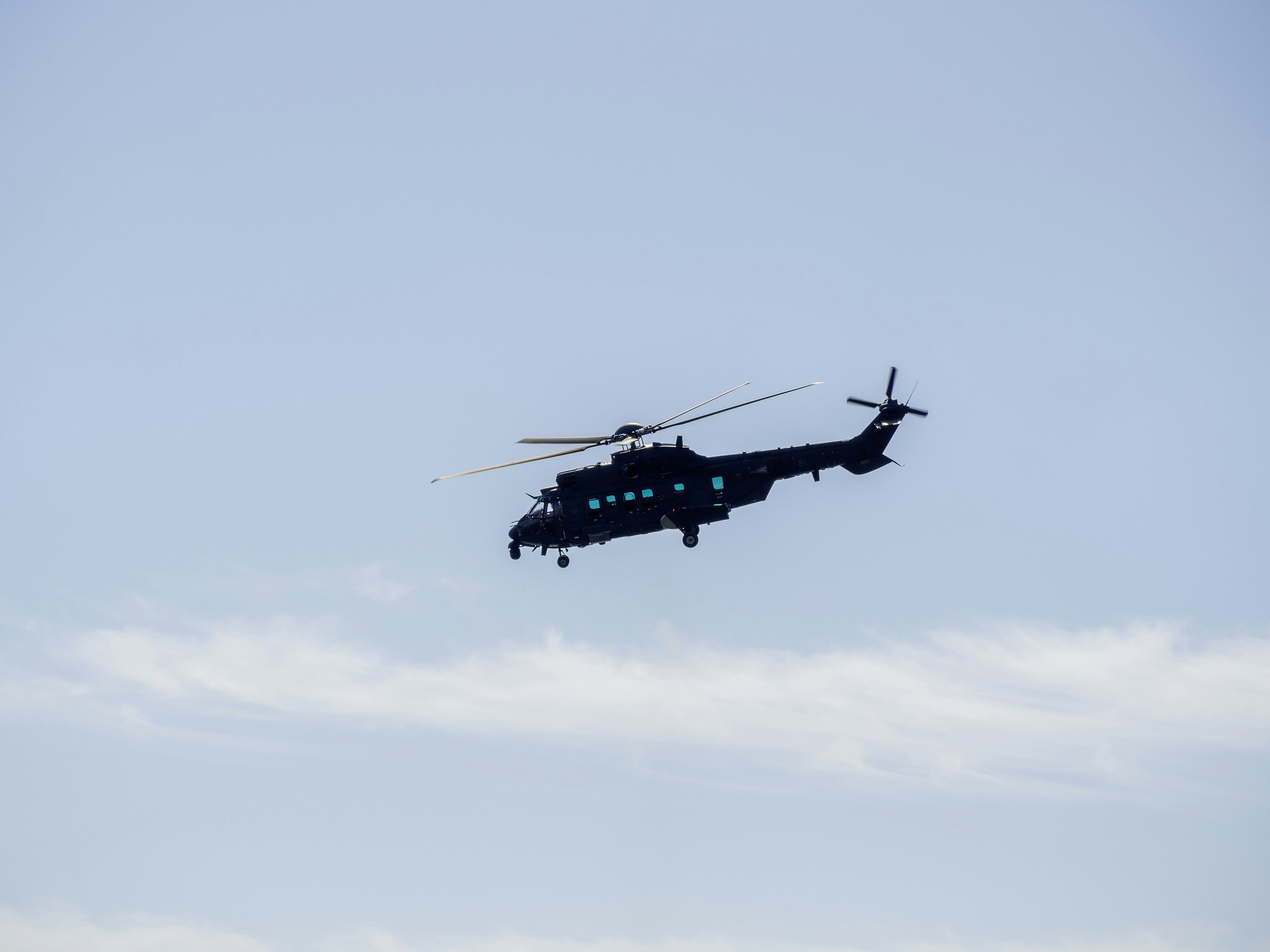 Silhouette of a military helicopter gliding above wispy clouds