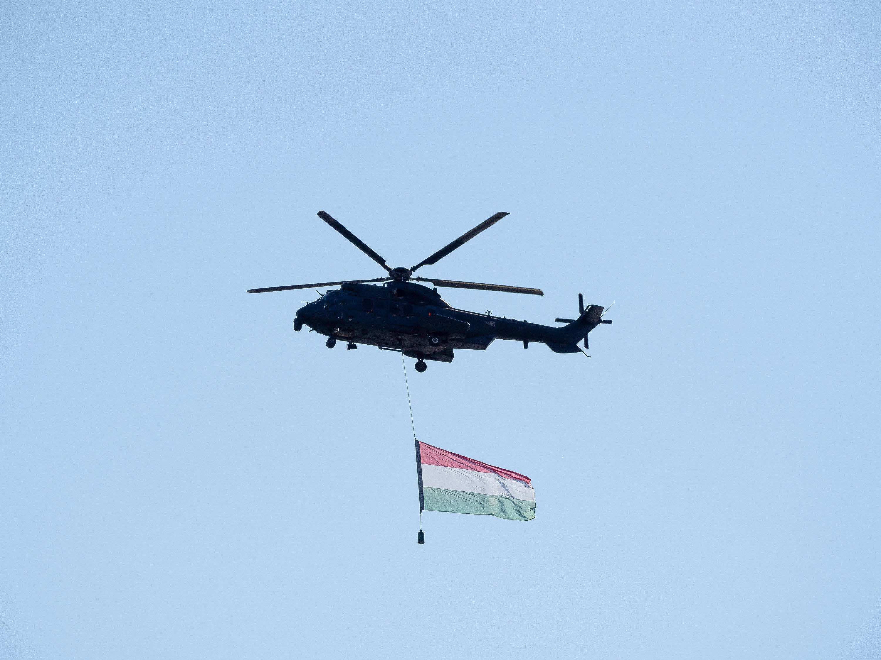 Hungarian Flag in Tow: A Helicopter Lift Over Open Sky