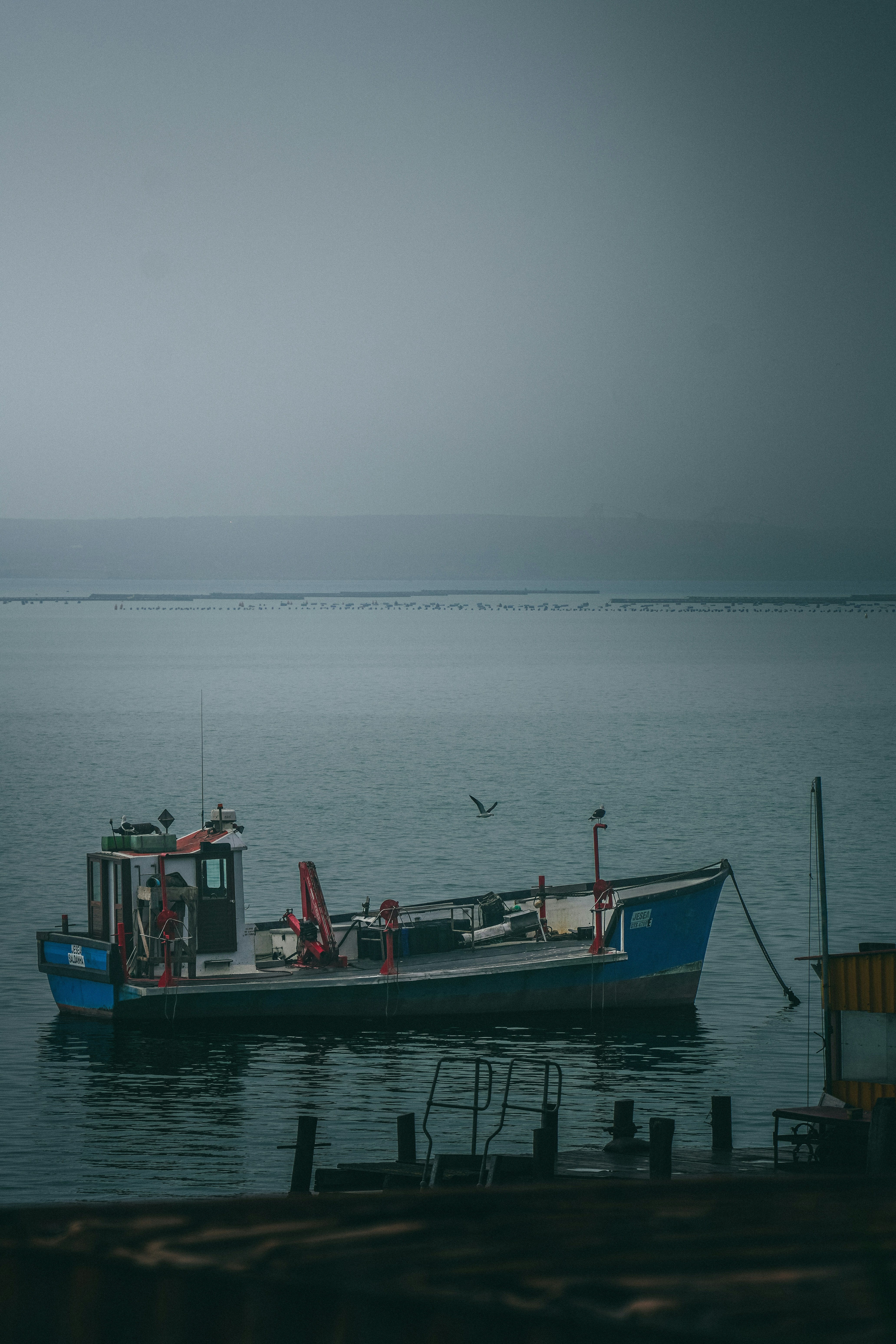 Harbor Ghosts: A Blue Boat Resting on Misty Still Waters
