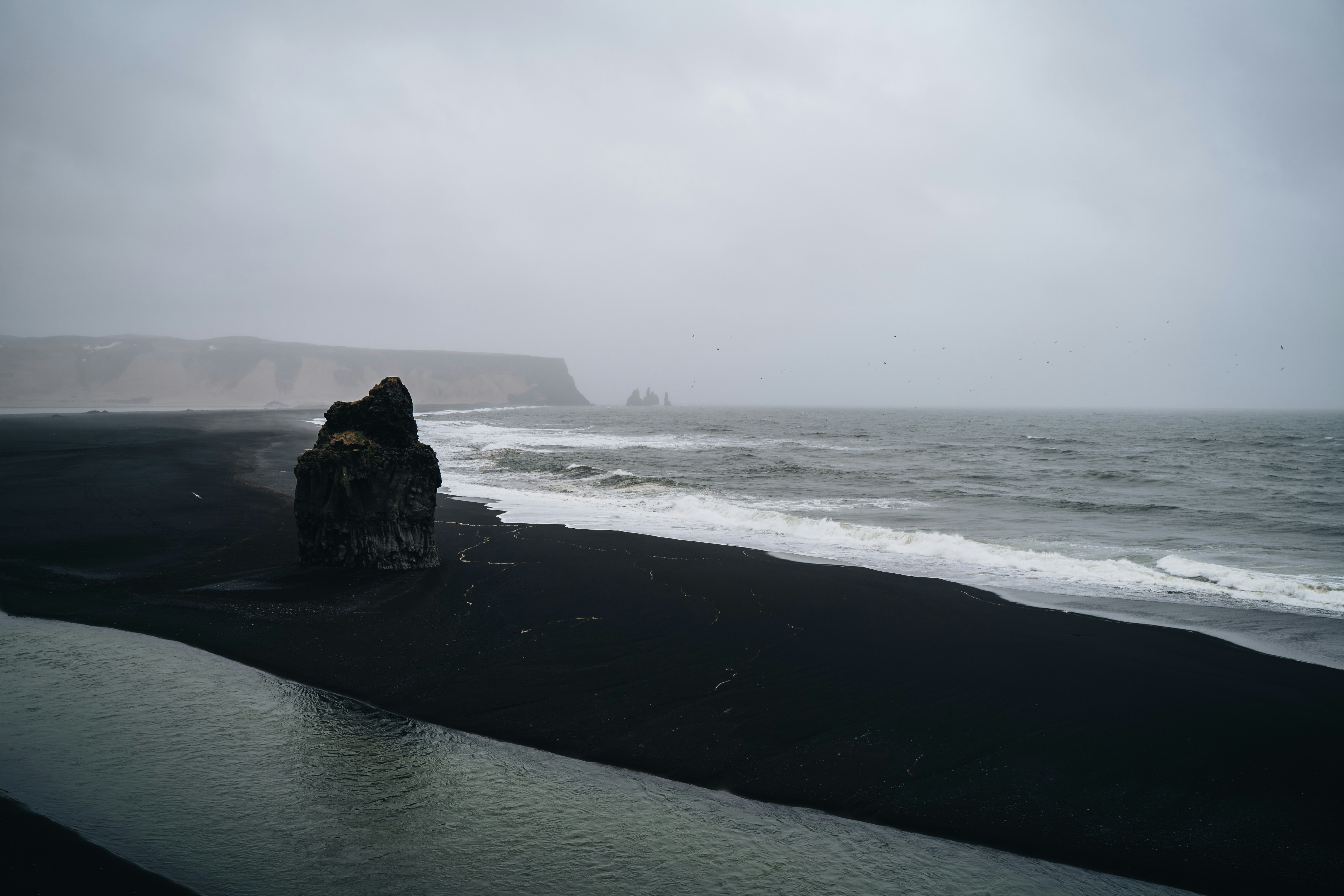 Dark Beach Standing Rock Beneath A Gray Distant Horizon