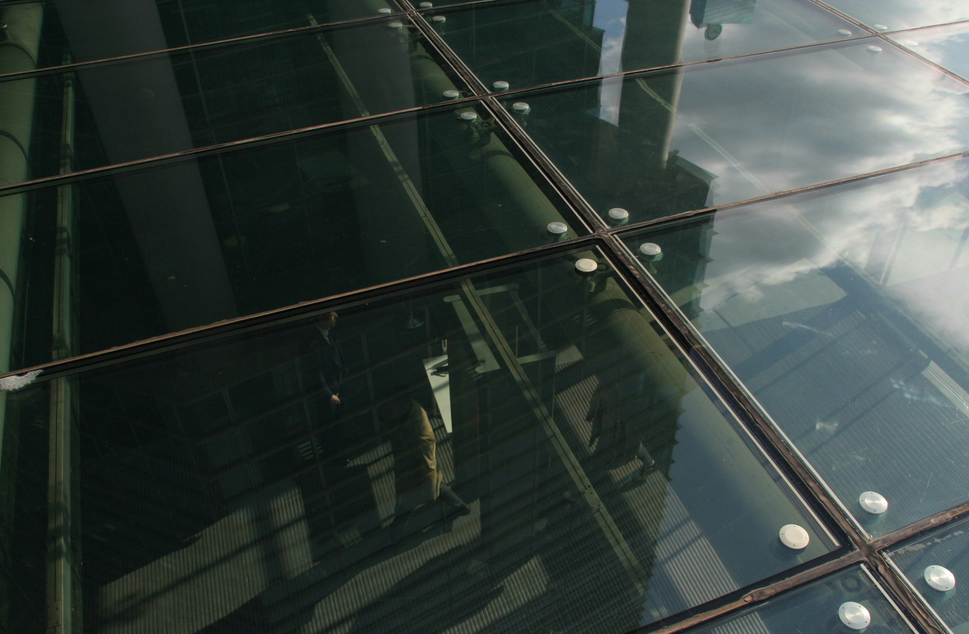 Glossy glass panels form a geometric walkway with metal supports and reflections creating a moody, urban abstraction.