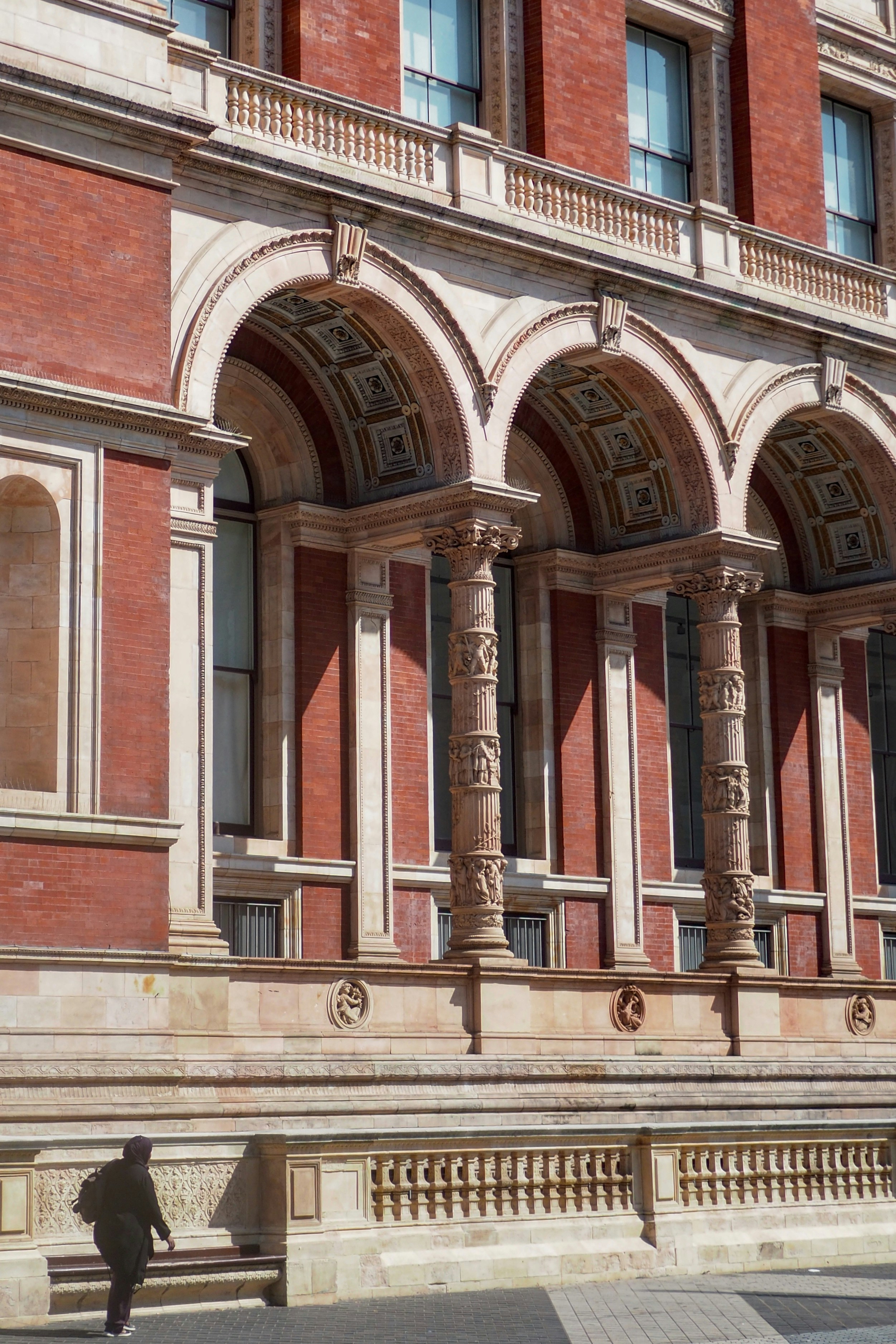 Arched facade of a brick building with carved columns and a distant figure descending the steps
