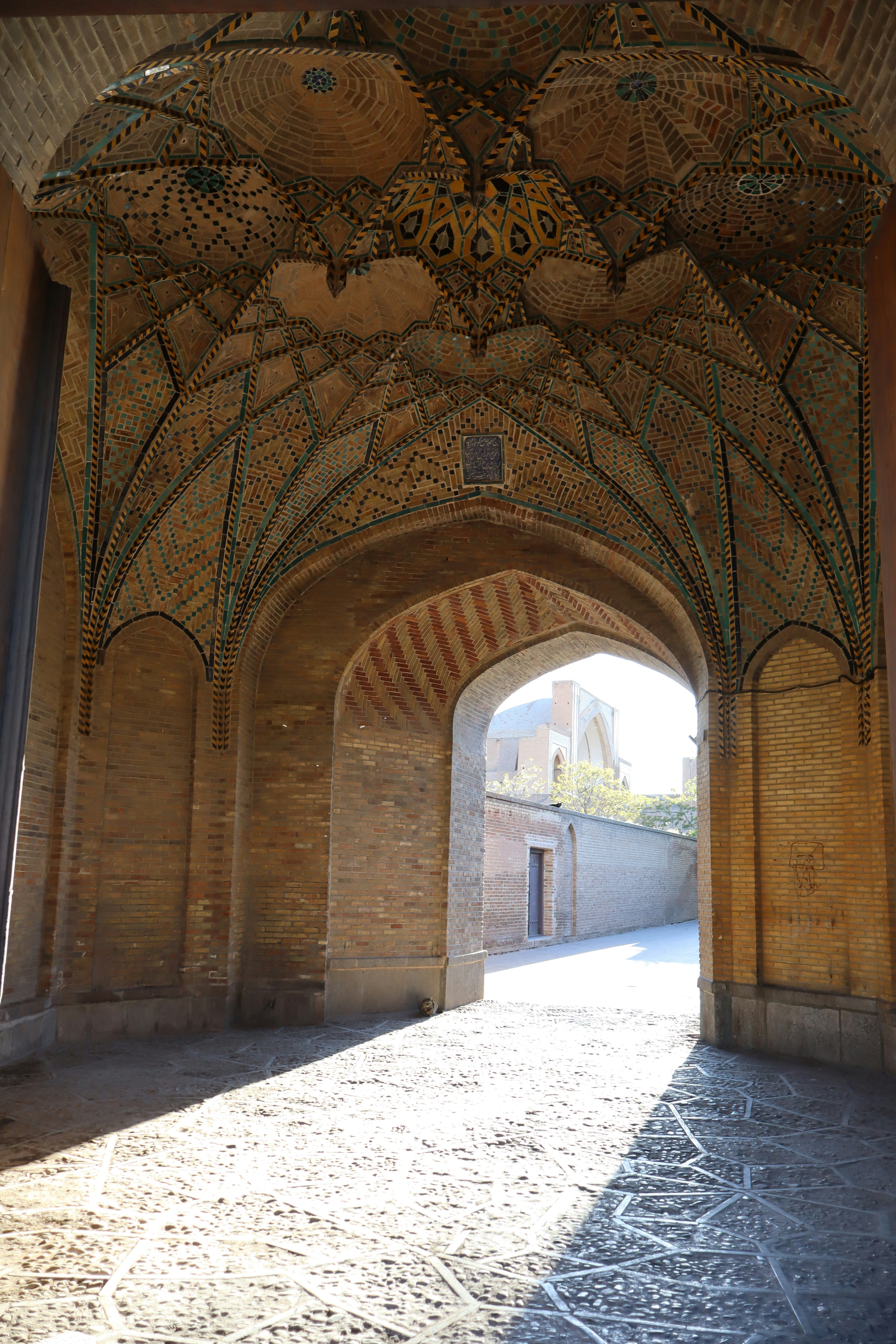 Sunlit Archway: Ancient Brick Vaults under Colorful Vaulted Carvings