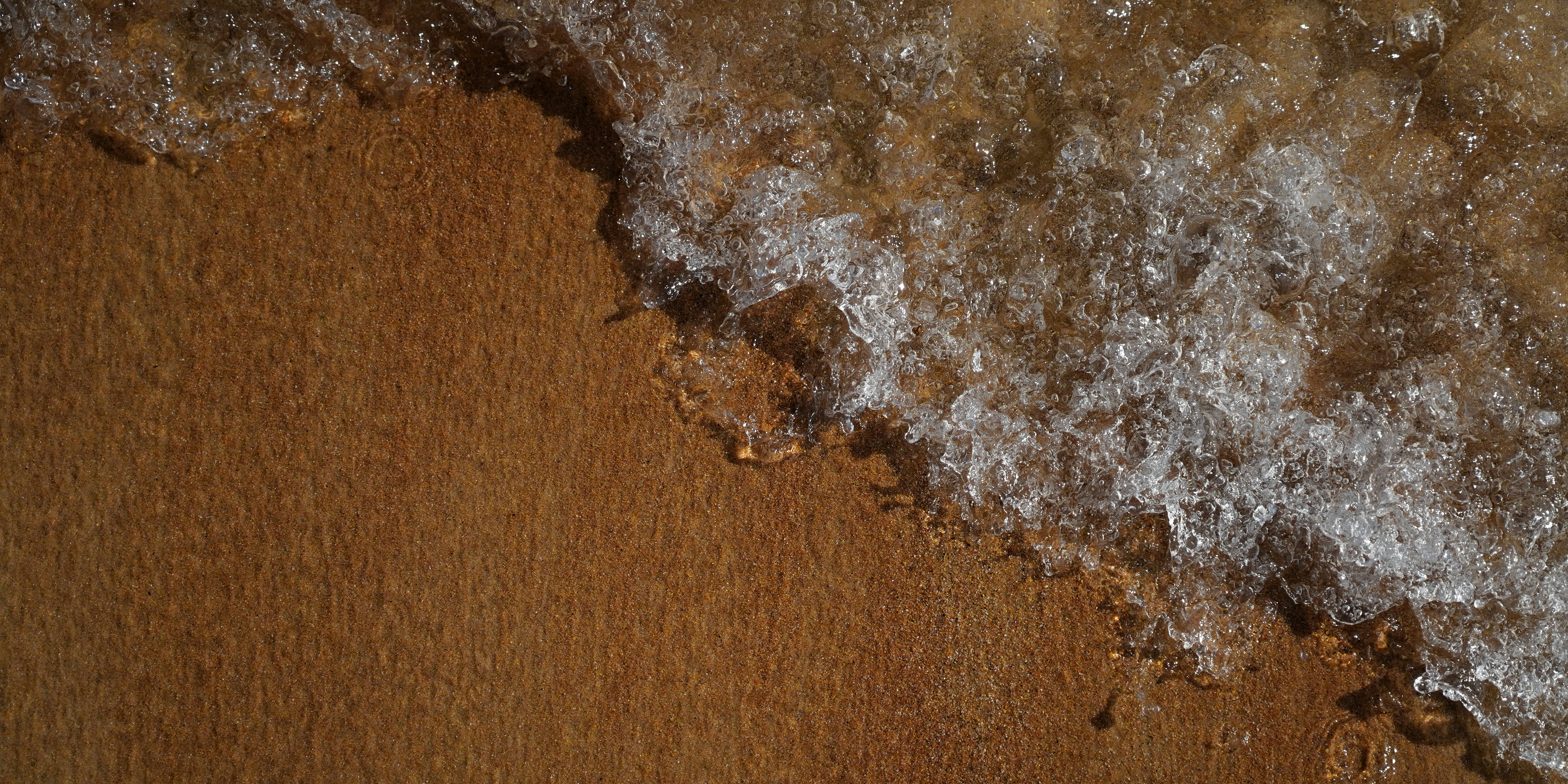 Foamy shoreline meeting warm sand