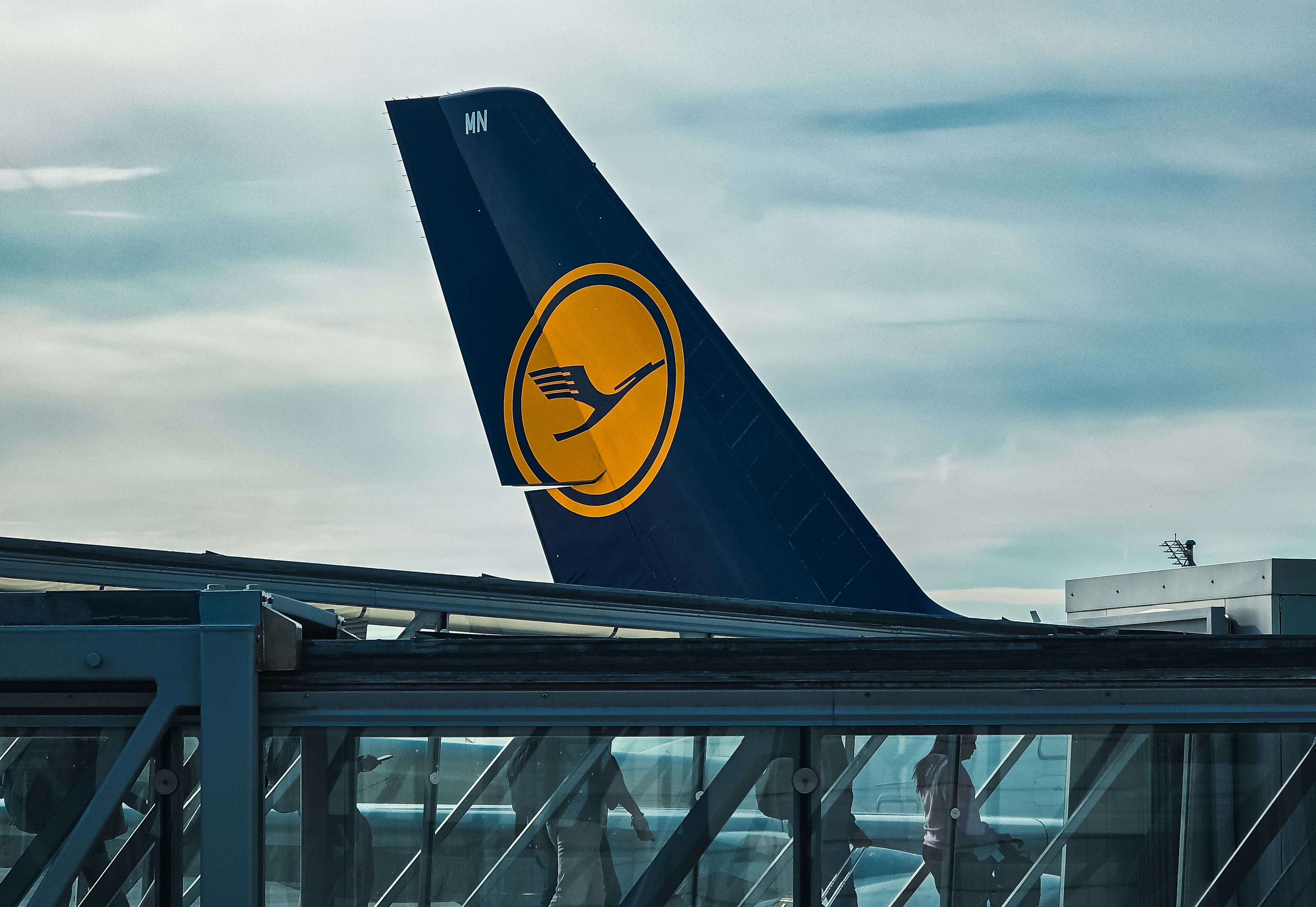 Close up view of the tailfin of a Lufthansa passenger aircraft, featuring the airline’s iconic yellow and dark blue crane logo. The distinctive aircraft tail design provides a clean representation of Lufthansa branding and European aviation.
