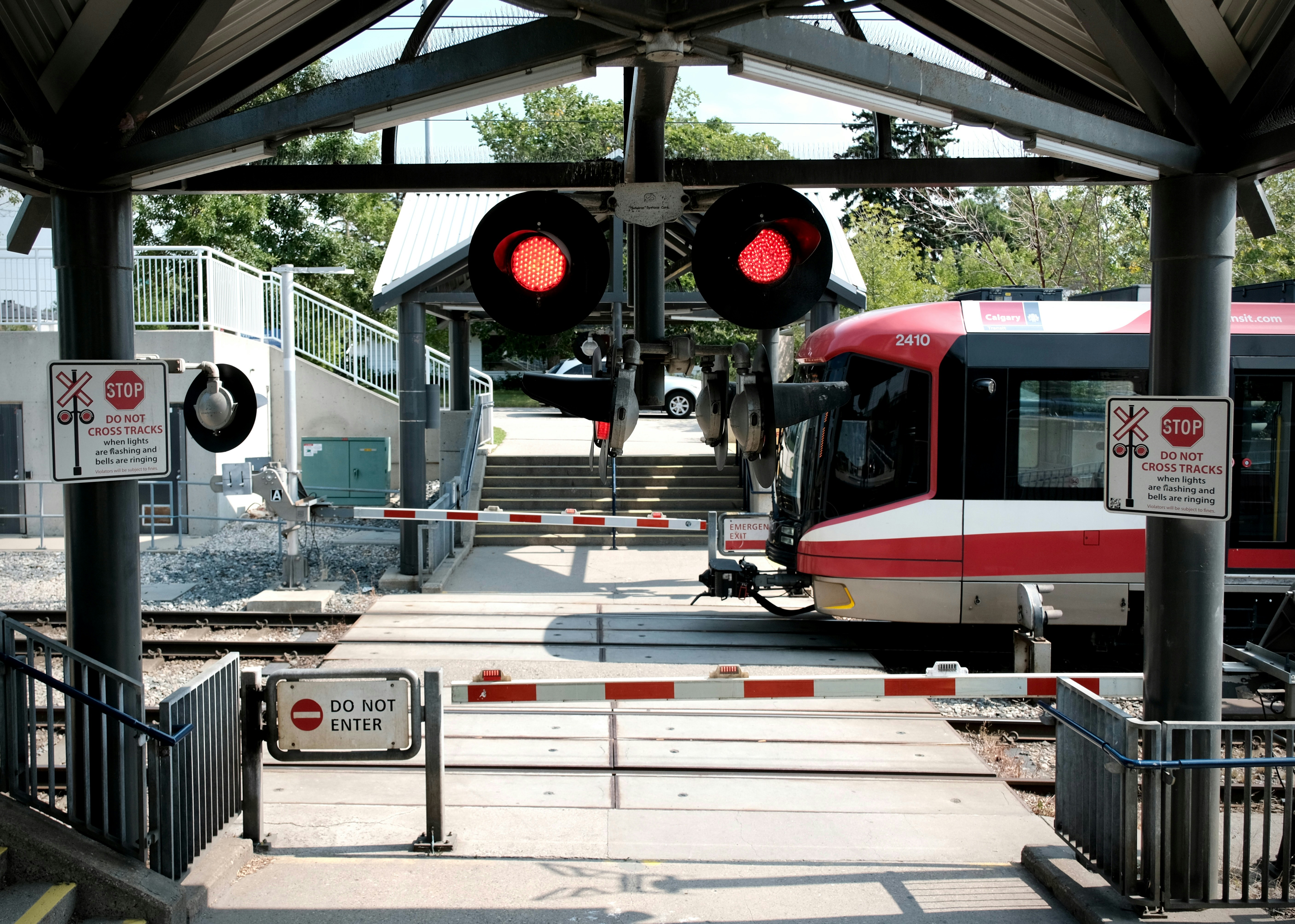 A red and white train at a railway crossing with flashing red warning lights