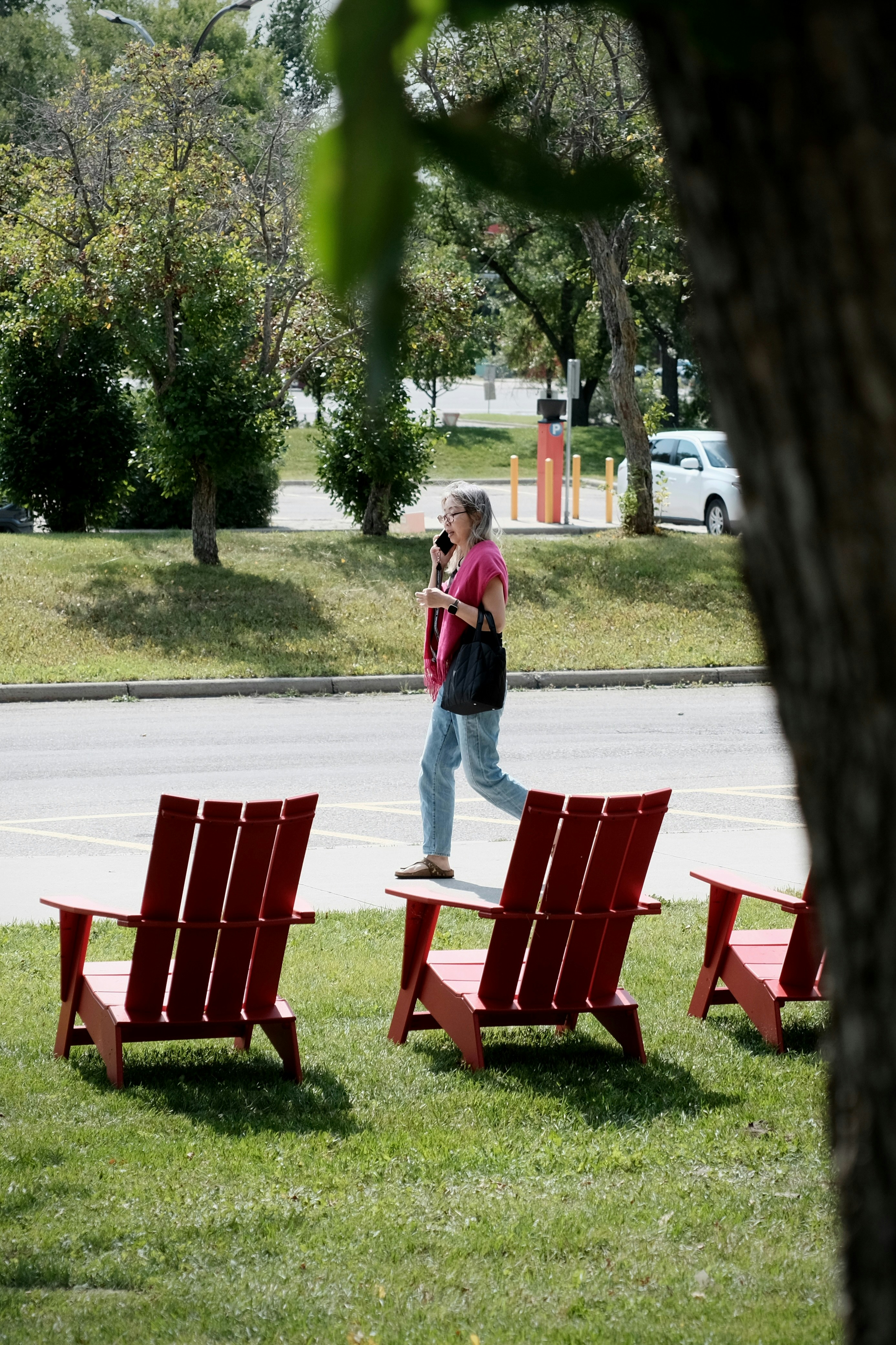 A lone passerby crosses the park’s edge, framed by red Adirondack chairs