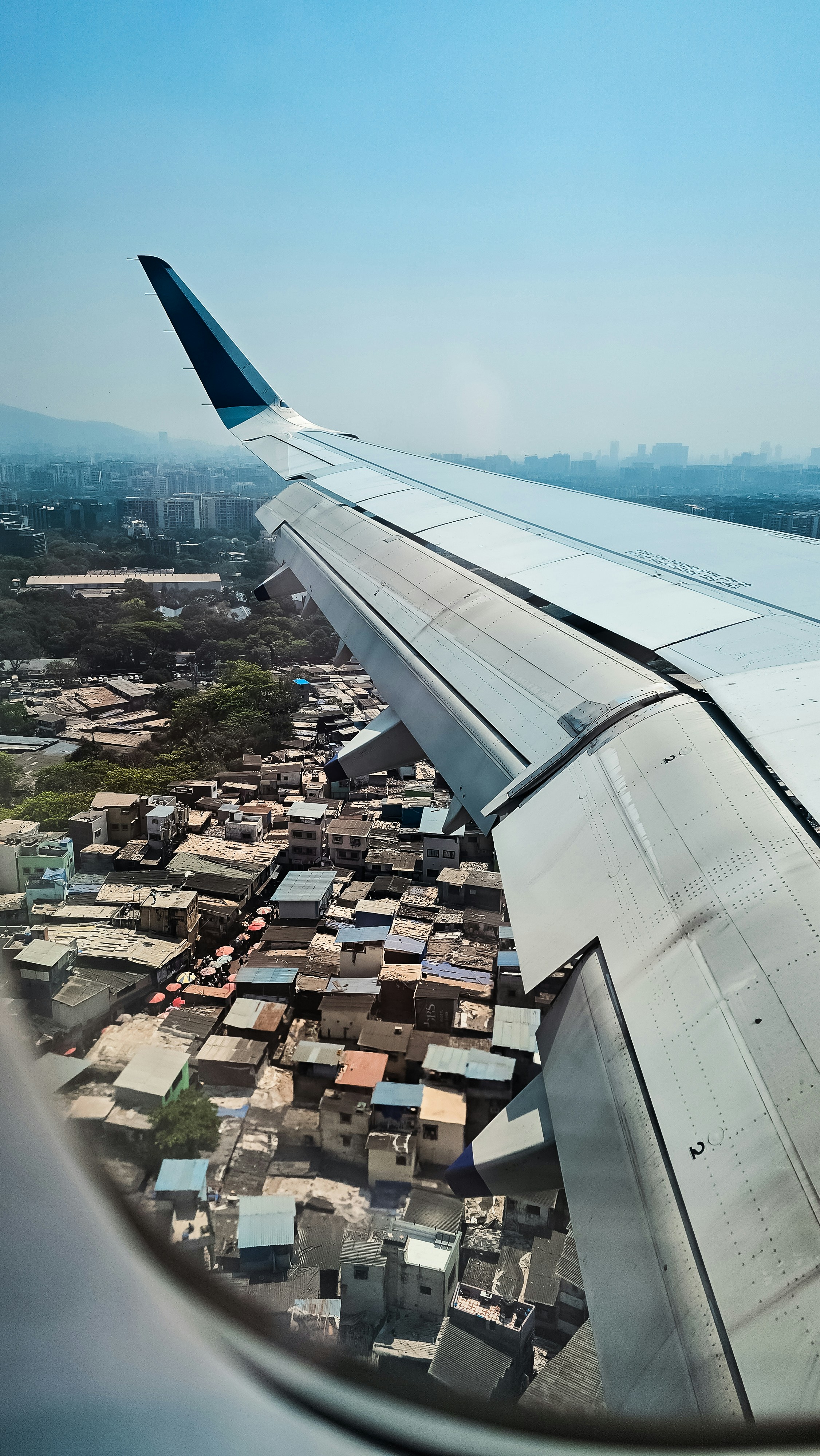 Low-altitude aerial view from my aircraft window capturing the tight approach over the densely packed urban informal settlements (slums) and industrial structures near Chhatrapati Shivaji Maharaj International Airport in Mumbai.