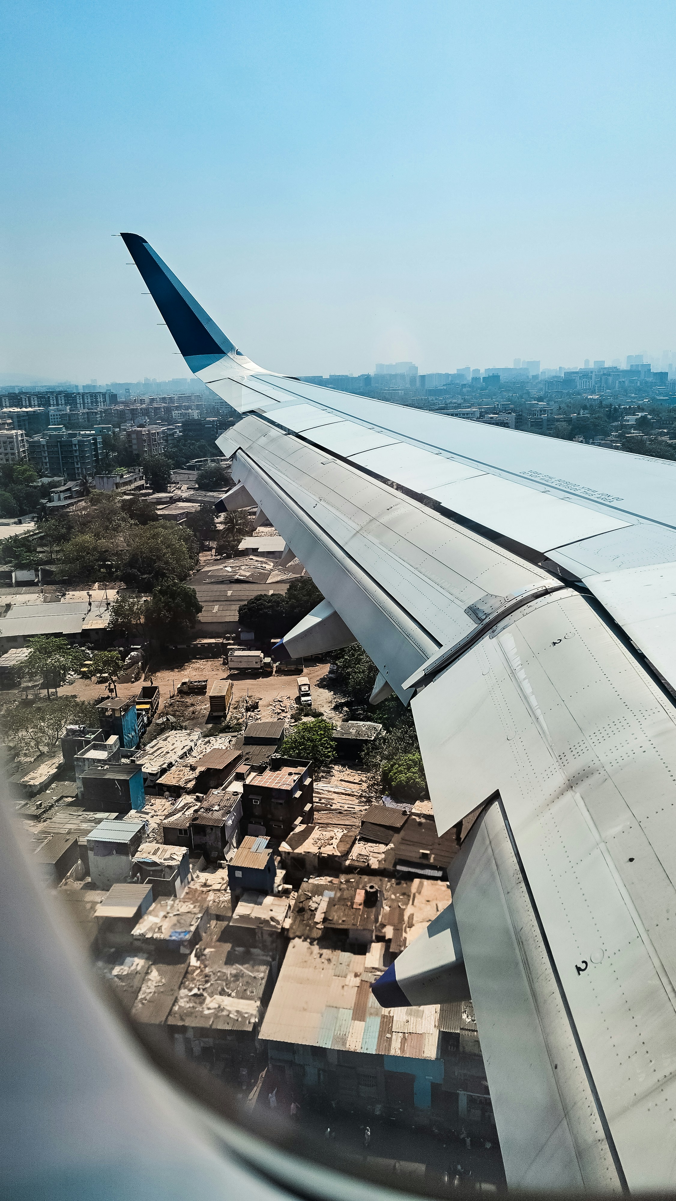 Low-altitude aerial view from my aircraft window capturing the tight approach over the densely packed urban informal settlements (slums) and industrial structures near Chhatrapati Shivaji Maharaj International Airport in Mumbai.