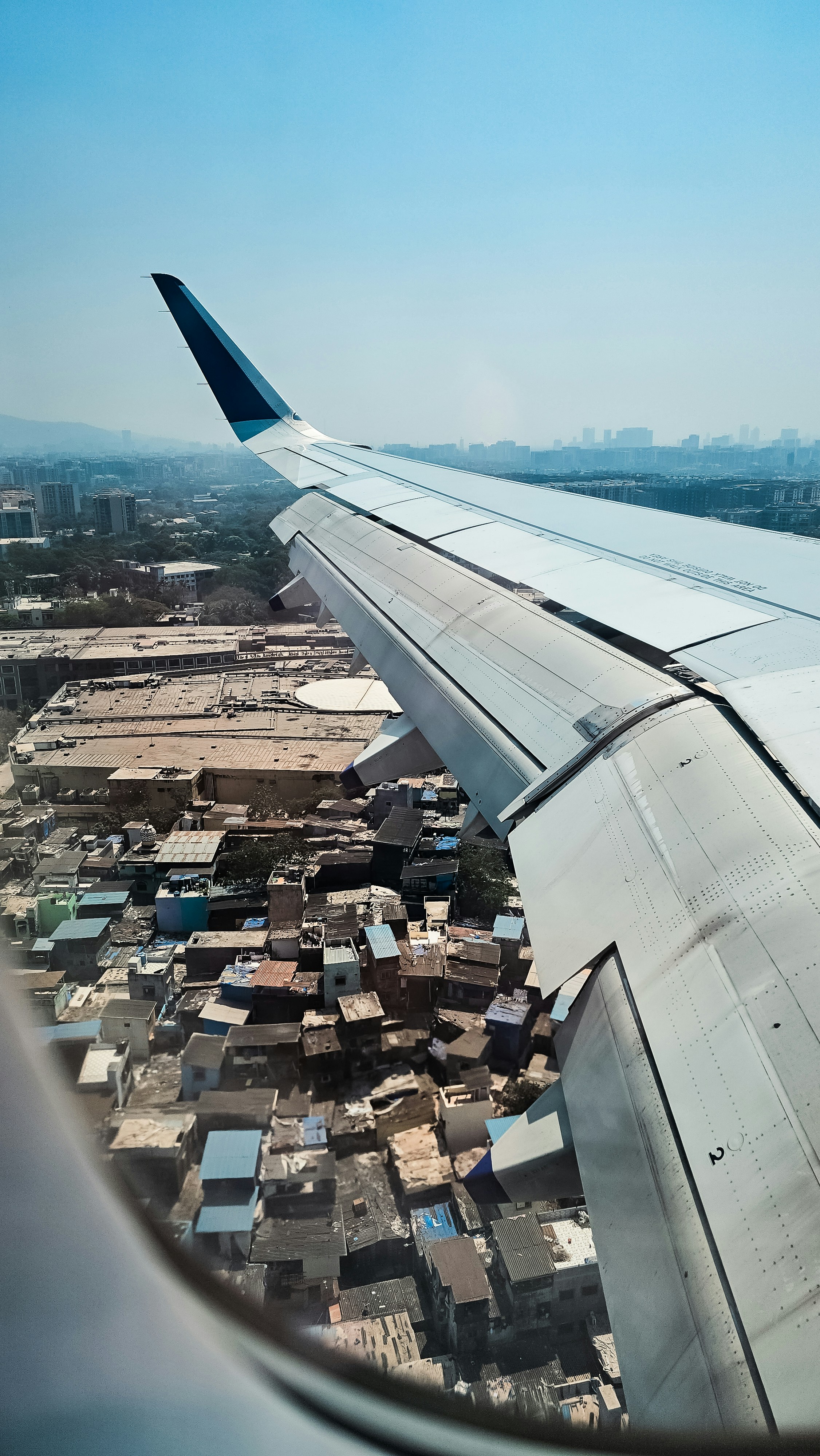 Low-altitude aerial view from my aircraft window capturing the tight approach over the densely packed urban informal settlements (slums) and industrial structures near Chhatrapati Shivaji Maharaj International Airport in Mumbai.