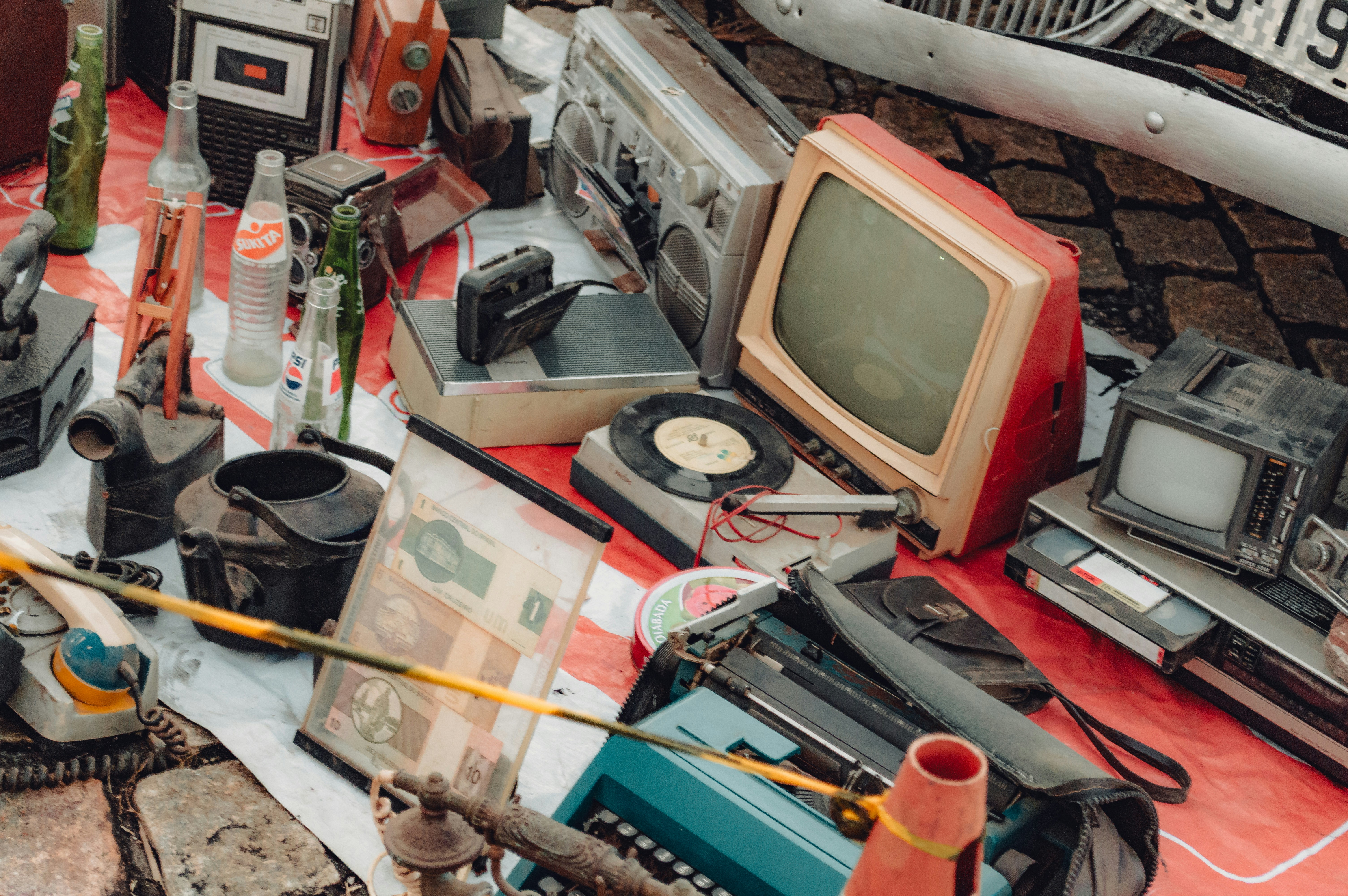 Vintage electronics, a typewriter, and glass bottles displayed on a red and white cloth
