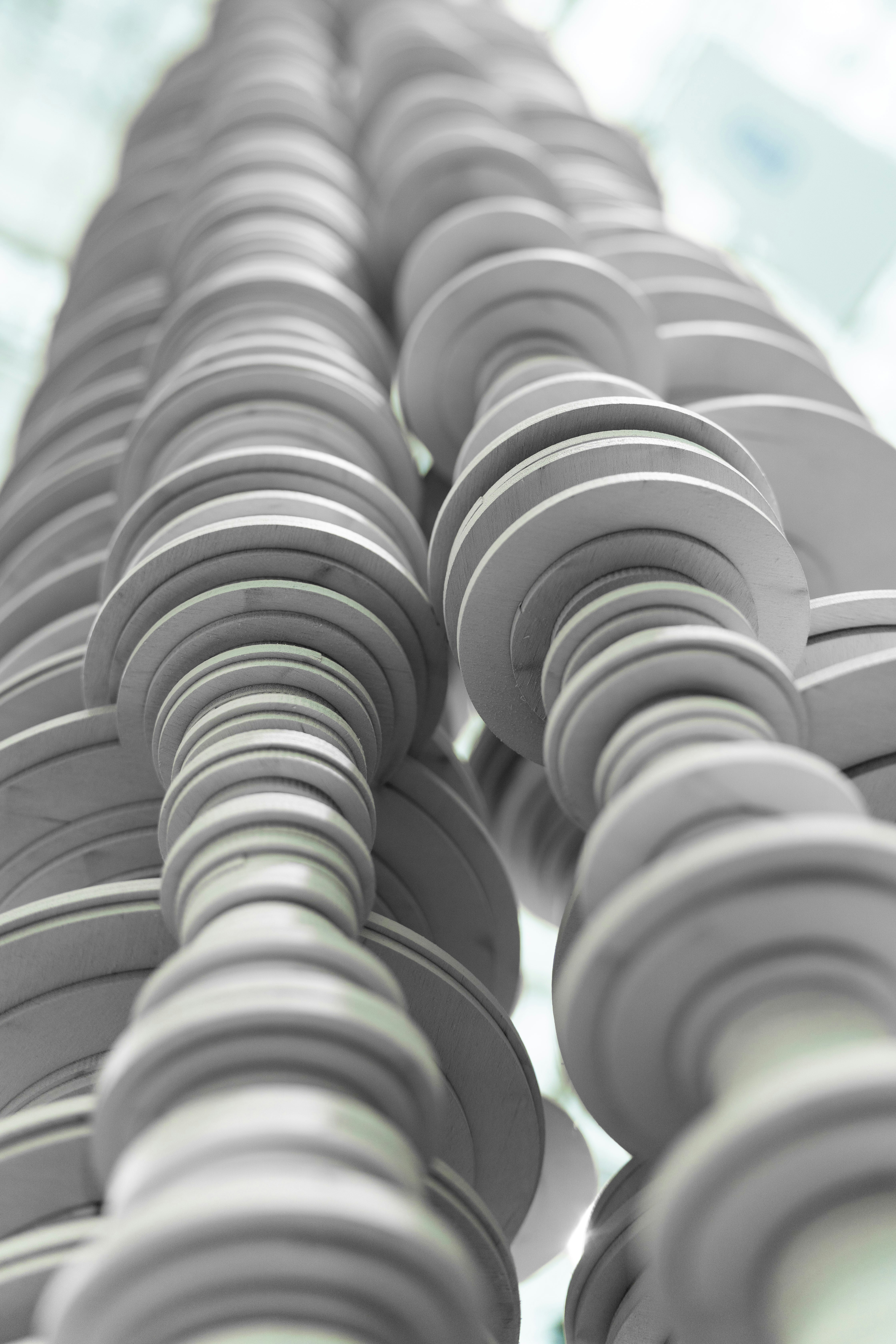 Close-up of a vertical arrangement of stacked grey circular discs, forming a repeated, spiral-like pattern with soft shading and depth. A minimalist, abstract composition highlighting texture and repetition.