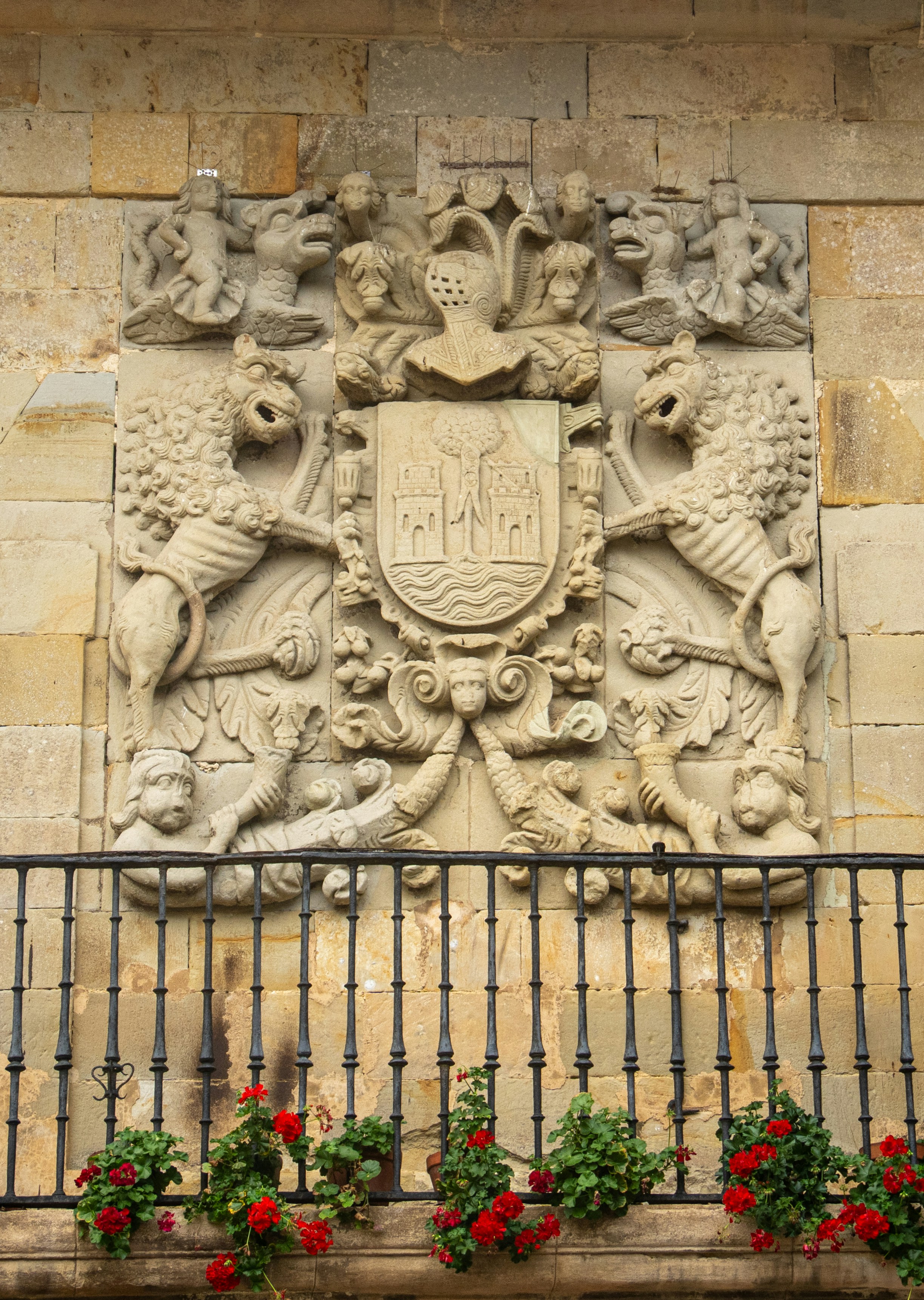 Emblem in Stone: A Regal Crest Overlooking a Balcony of Red Blooms