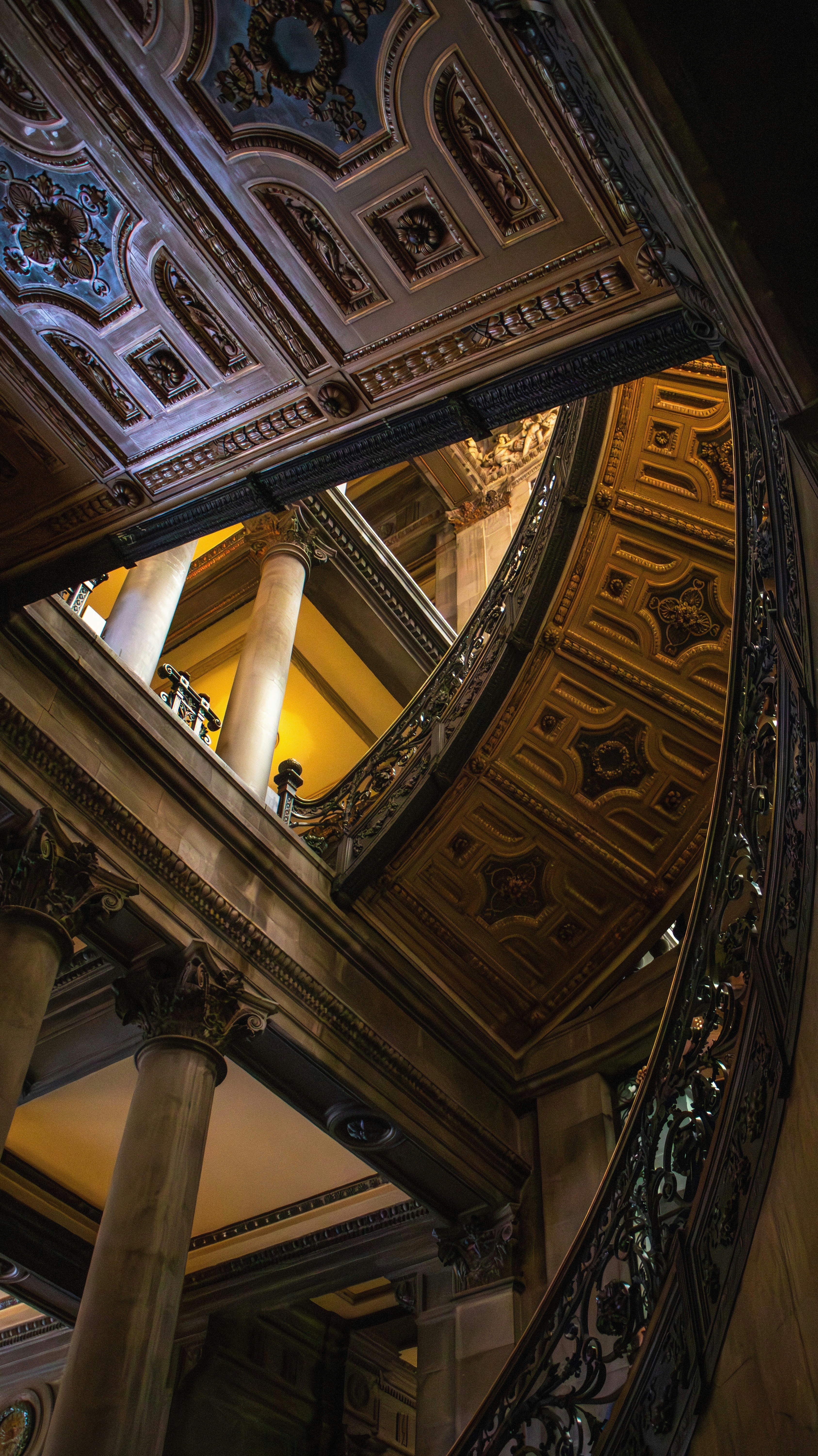 Intricate interior with a sweeping wrought-iron staircase and decorative ceiling panels in warm amber lighting.