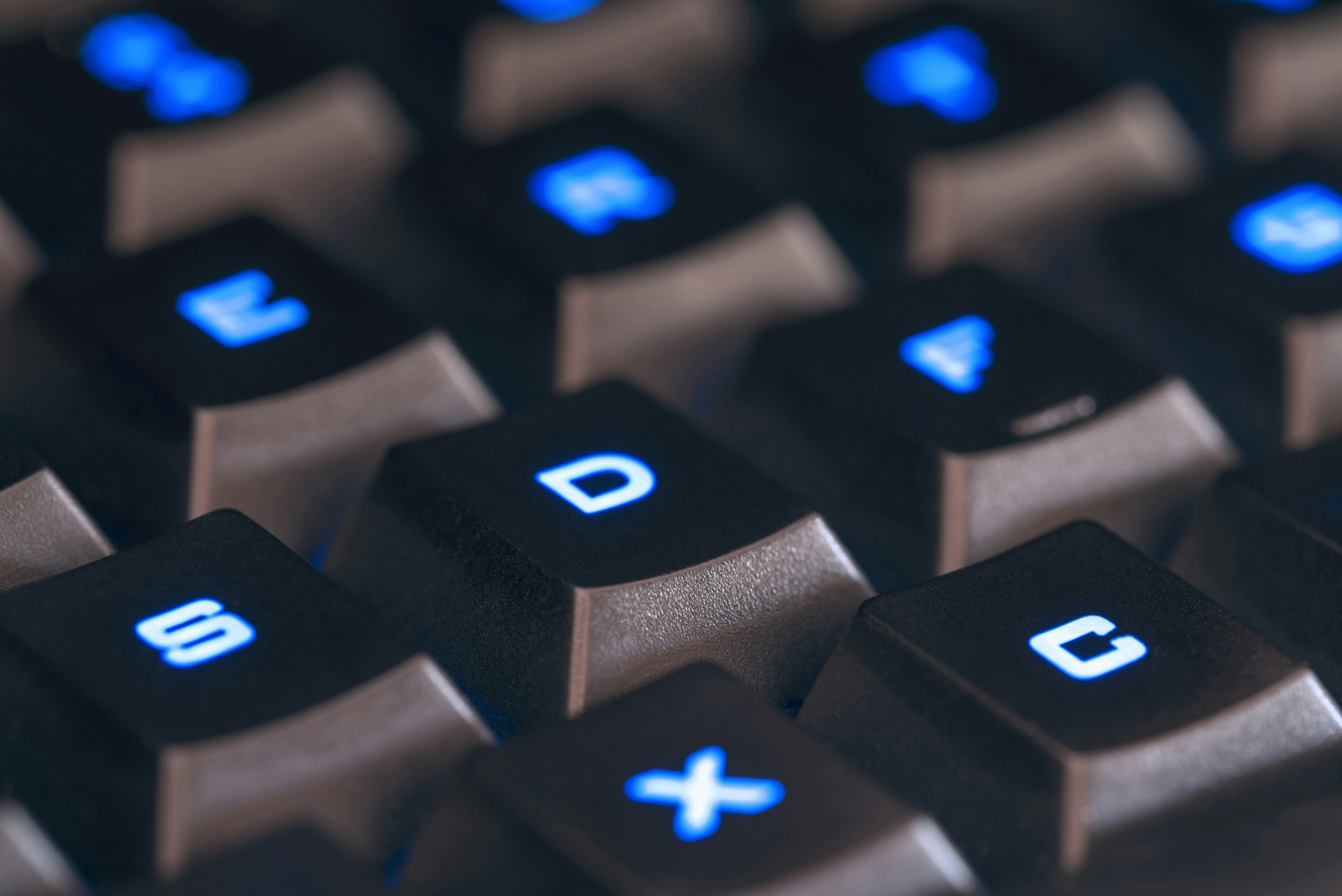Close-up of illuminated keyboard keys with blue-dyed letters and soft bokeh in the background, emphasizing the glowing characters and metallic keycaps.