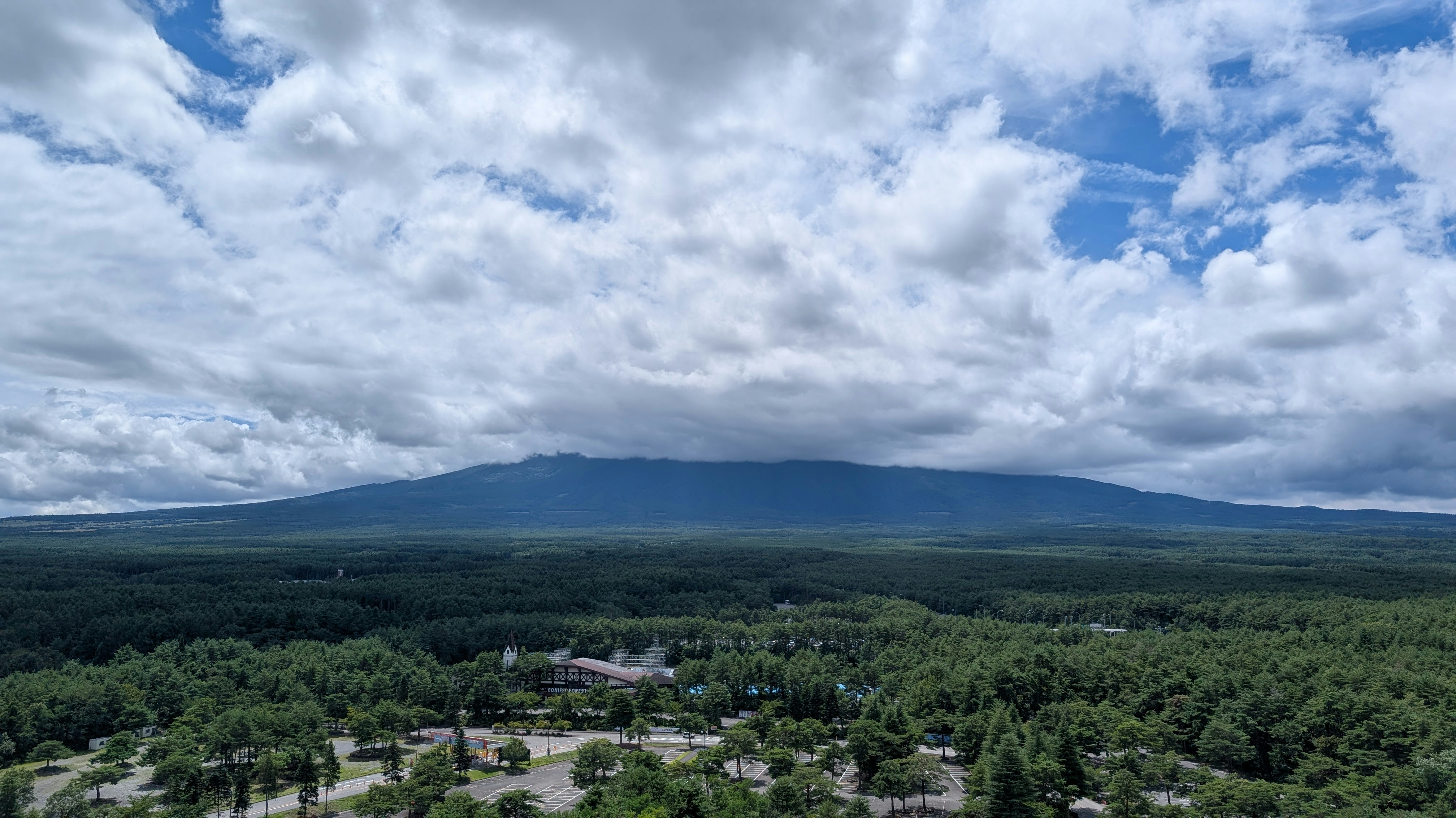 Expansive green plains stretch toward distant forested hills under a sky filled with thick clouds.