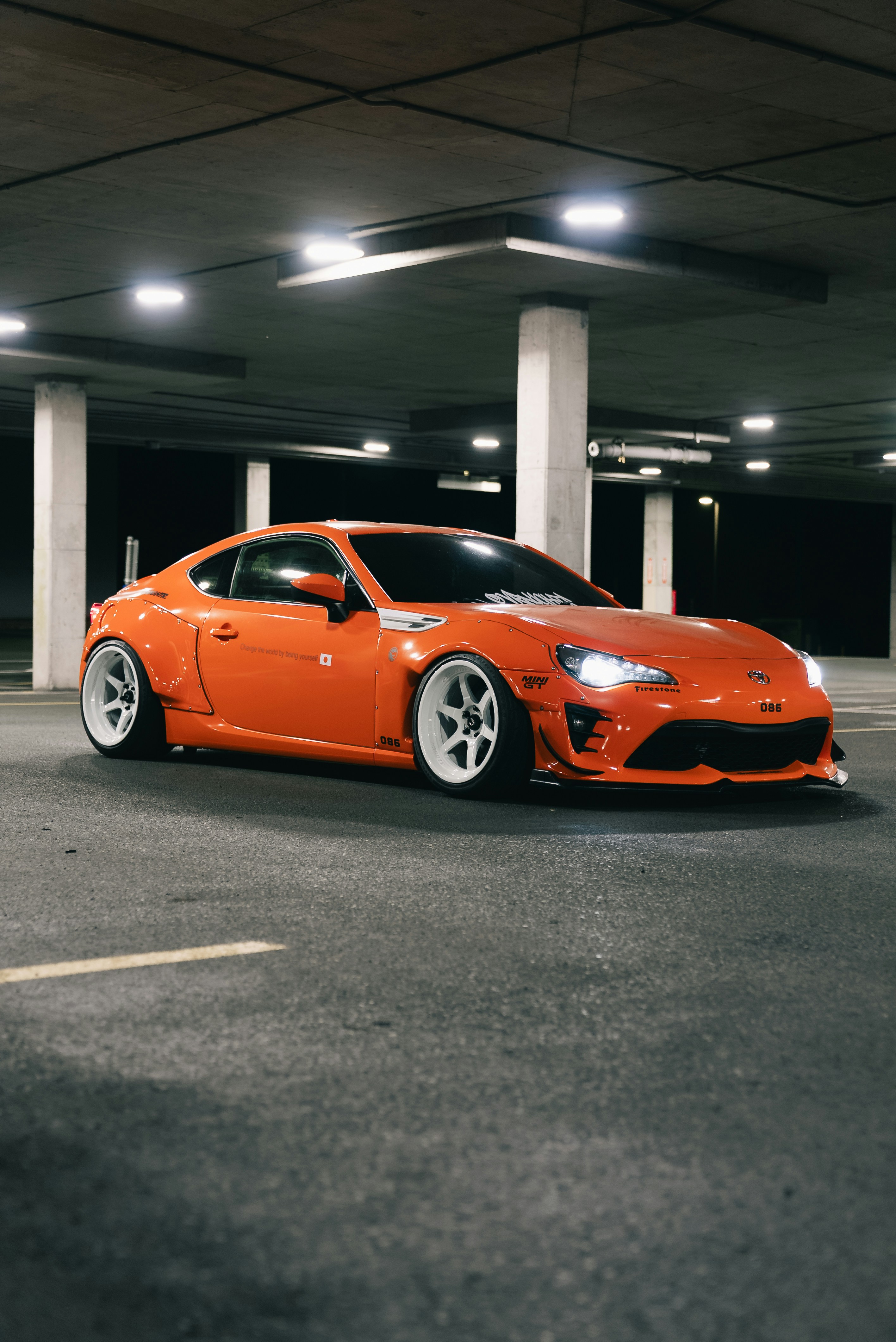 Orange racer under garage lights: low-angle spotlight on a tuned coupe