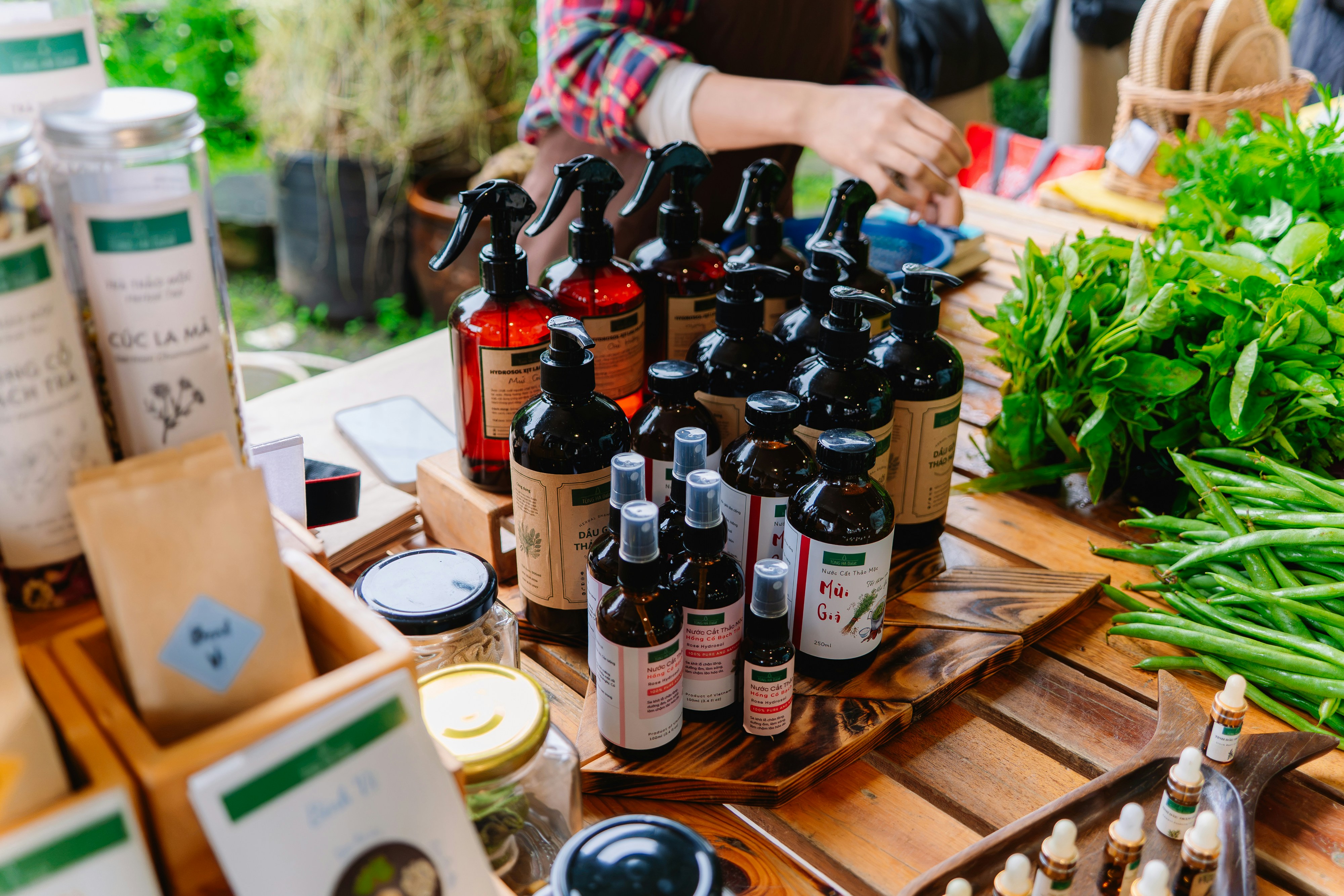 Close-up of a market stall displaying an array of bottles and jars, with fresh herbs in the background and wooden textures adding warmth.