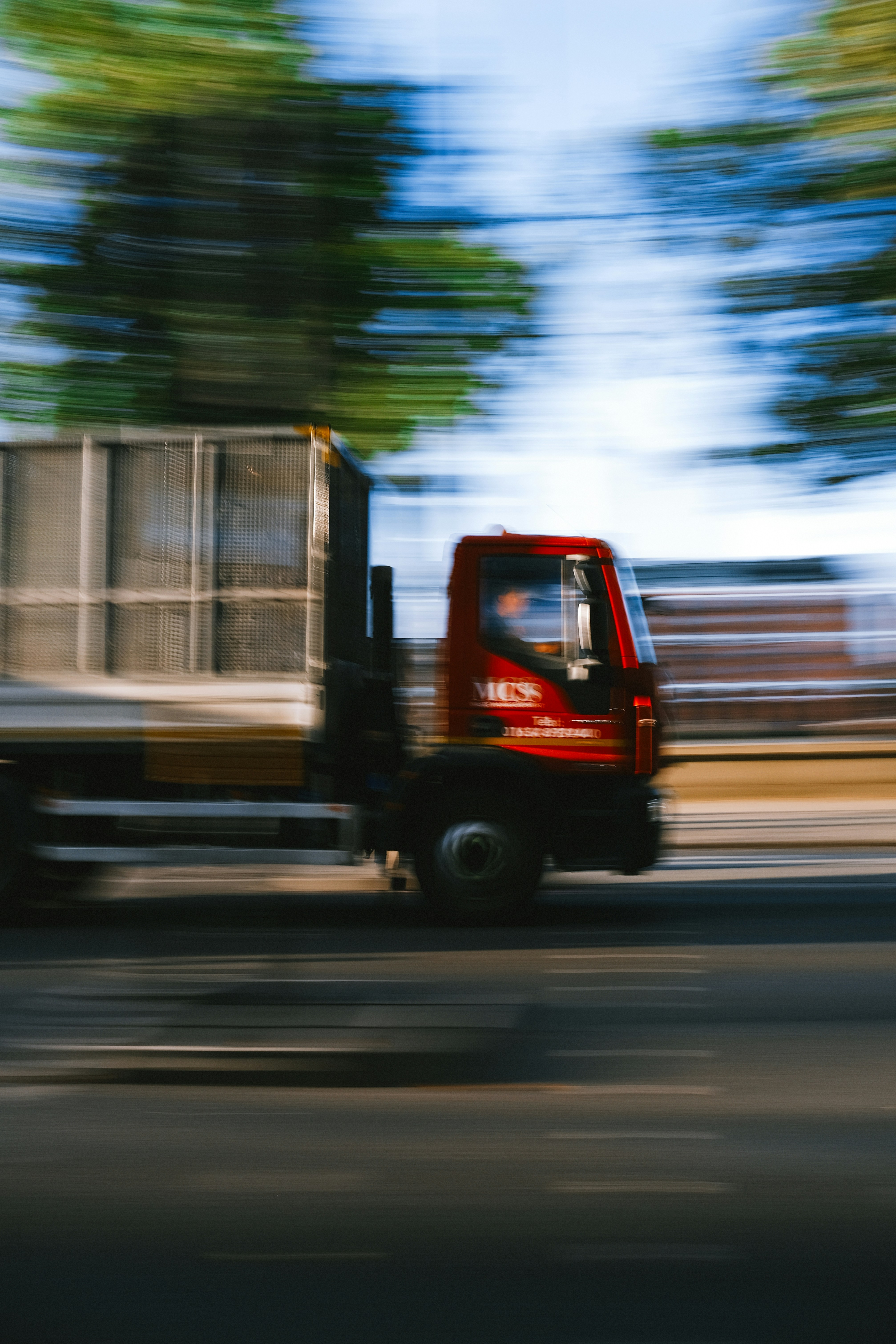 Blurred Freight: a red truck in motion along a sunlit street