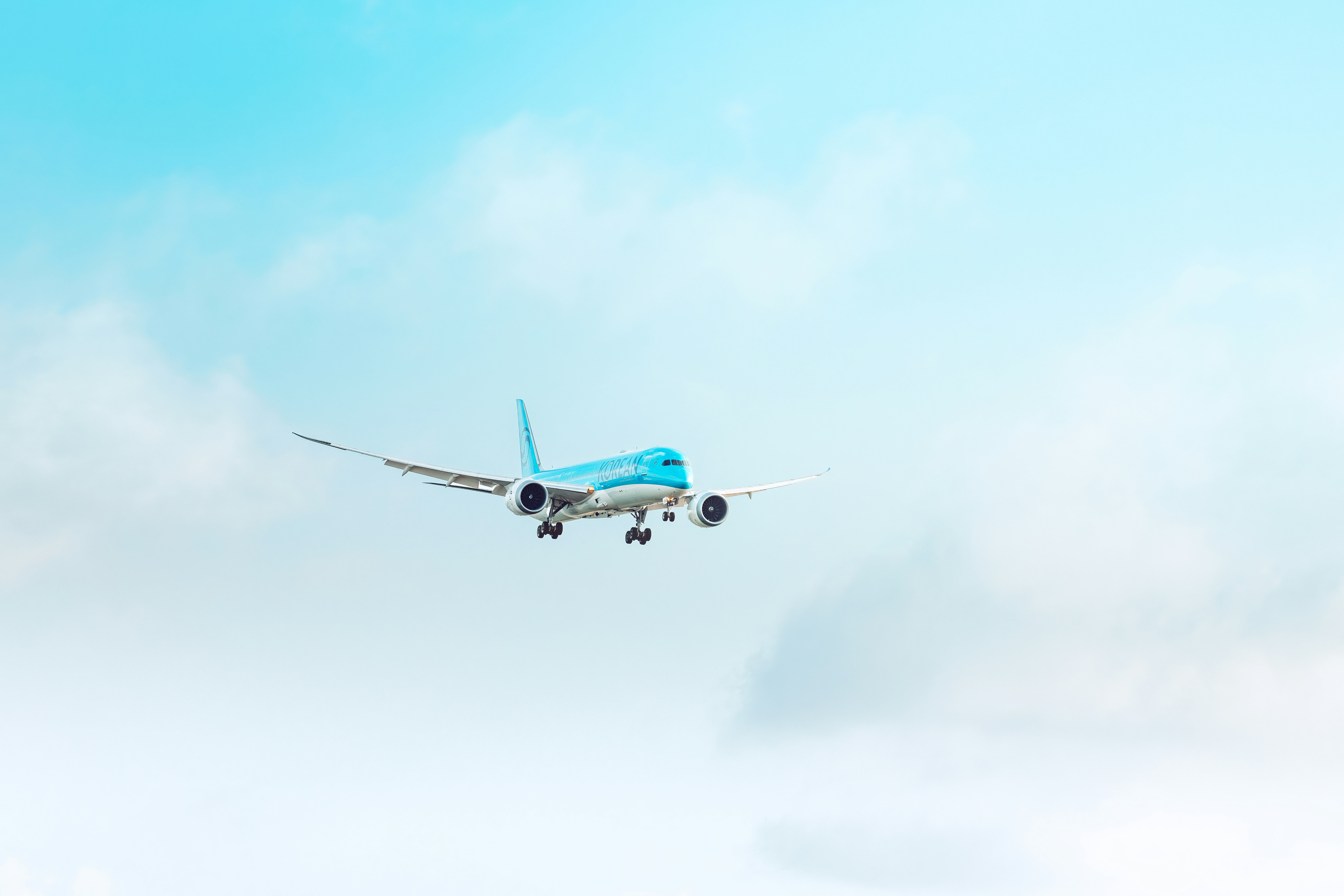 Blue airliner descending toward a pale blue sky with scattered clouds. A calm aviation moment captured mid-flight.