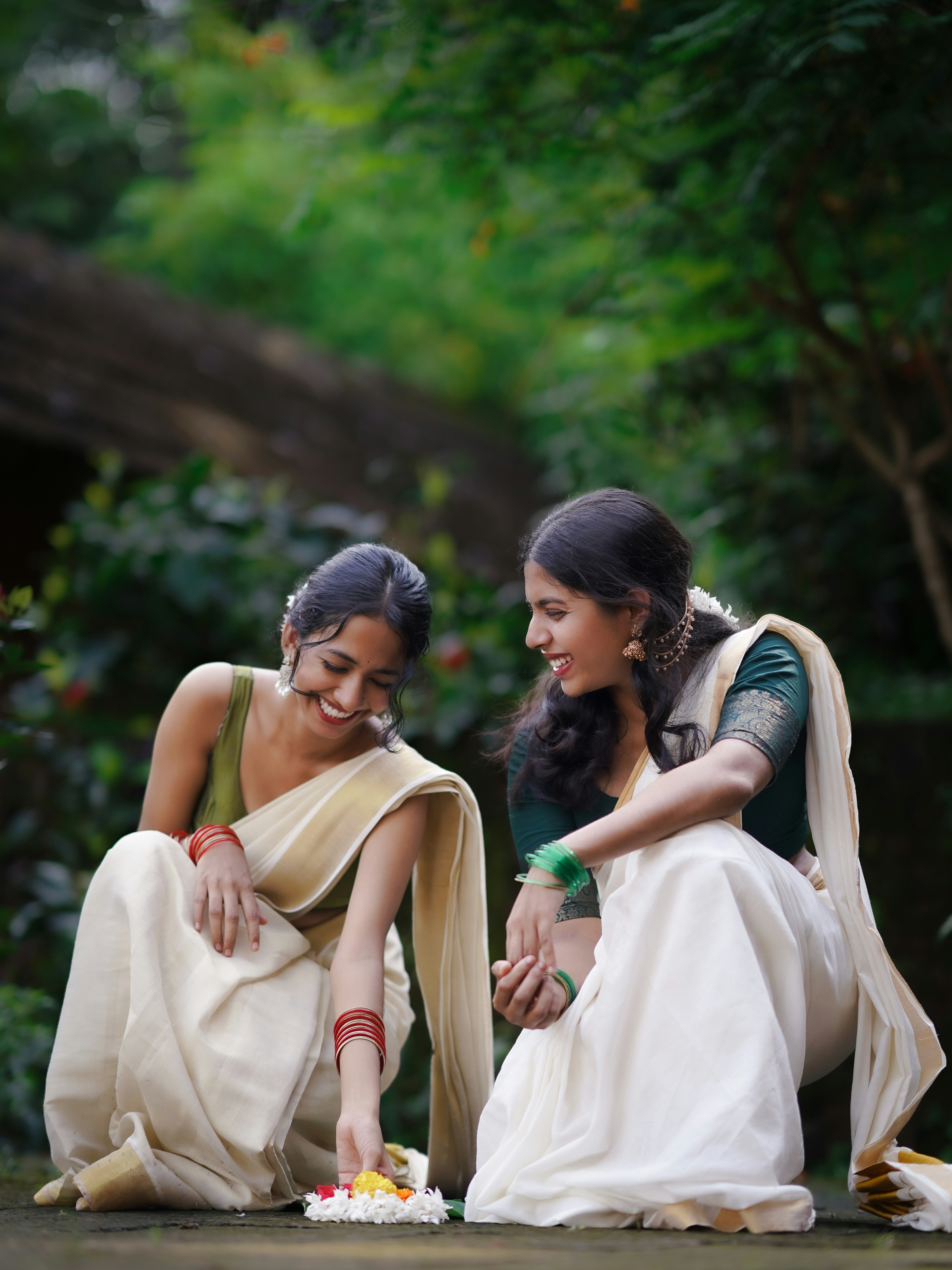 Two smiling women in traditional sari gathers flowers in a serene garden