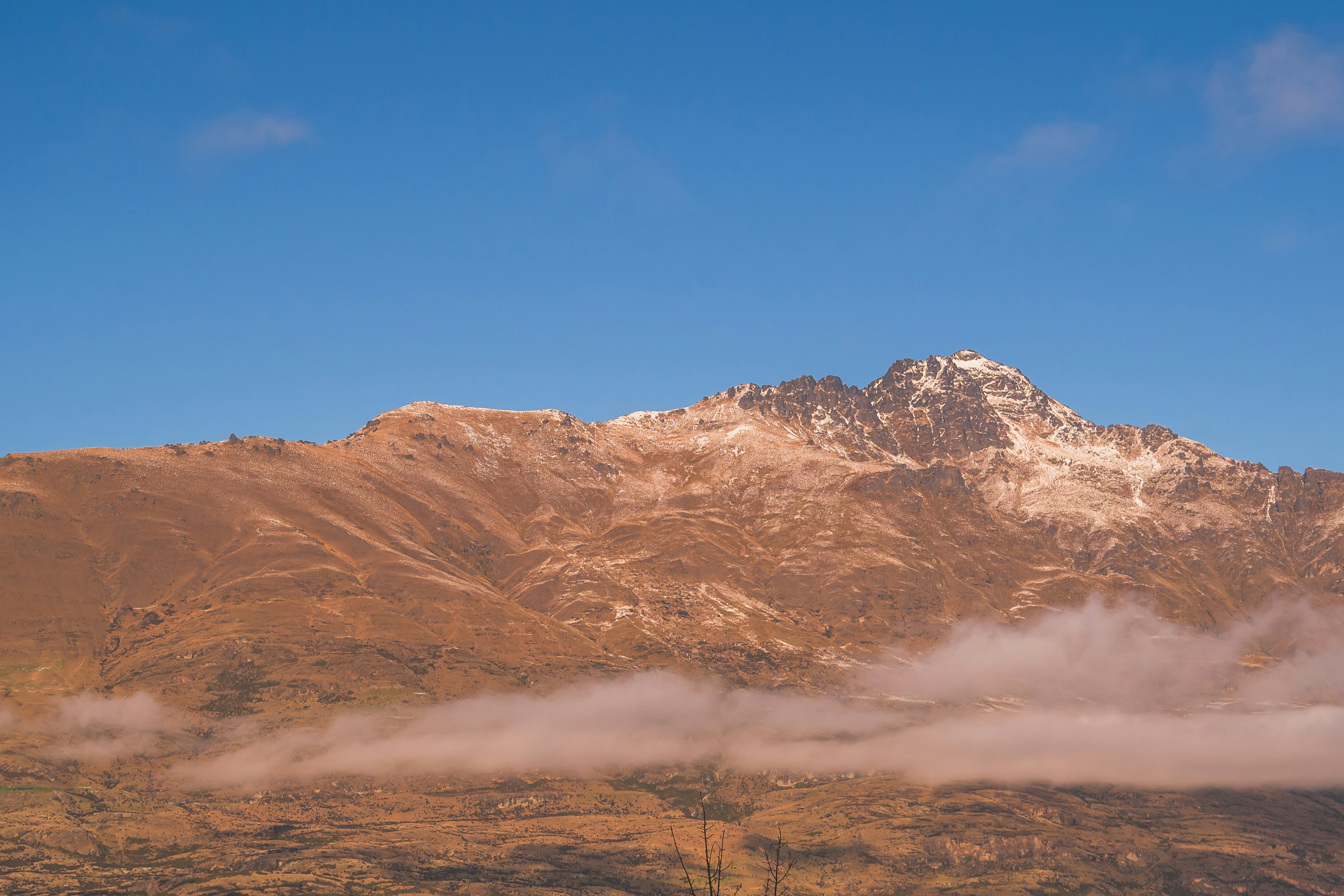 Snow-dusted mountain ridge rises beneath a blue sky with a low-lying cloud band across the valley.