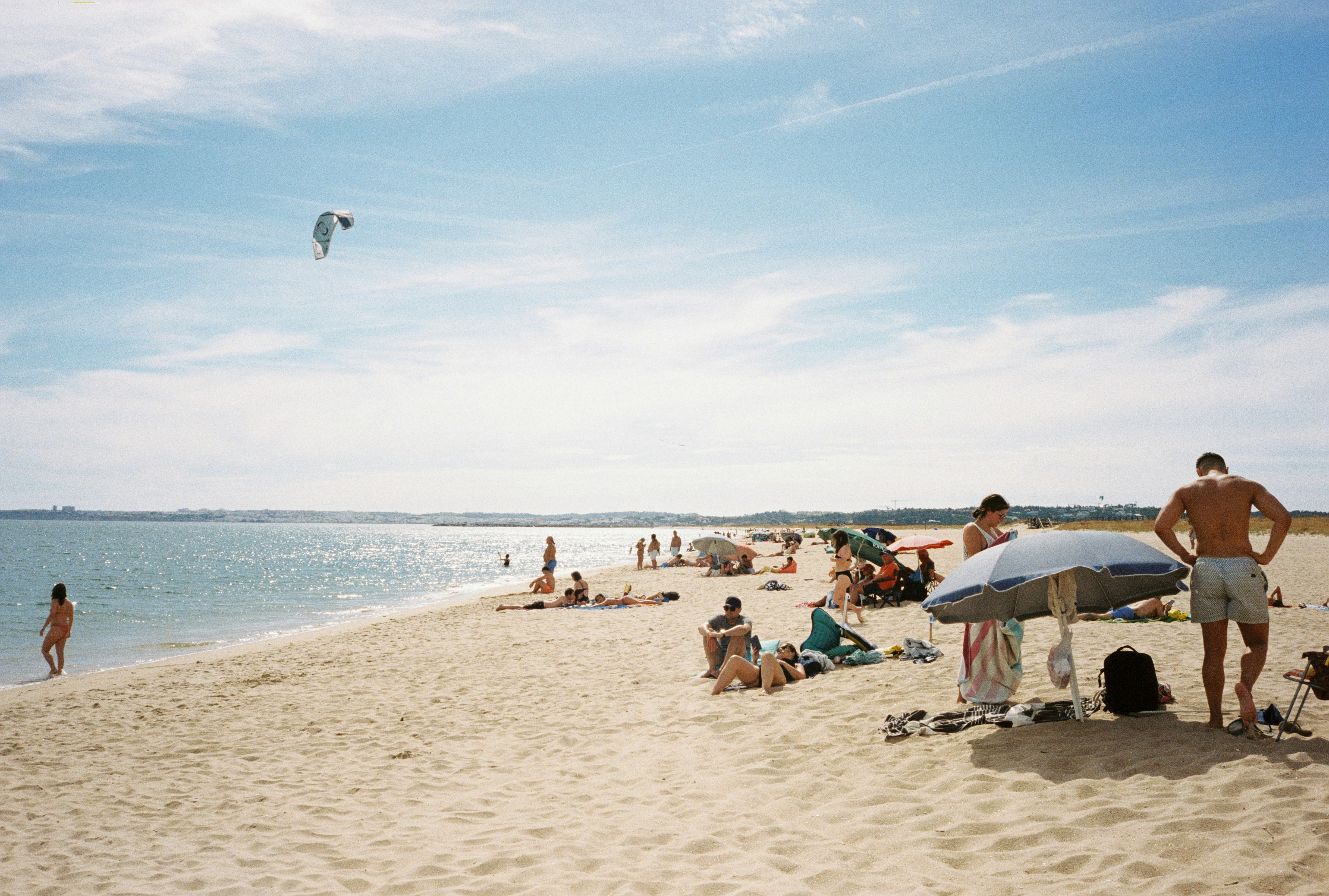 Sunlit Shoreline: Beachgoers and a Kite Surfer under a Bright Sky