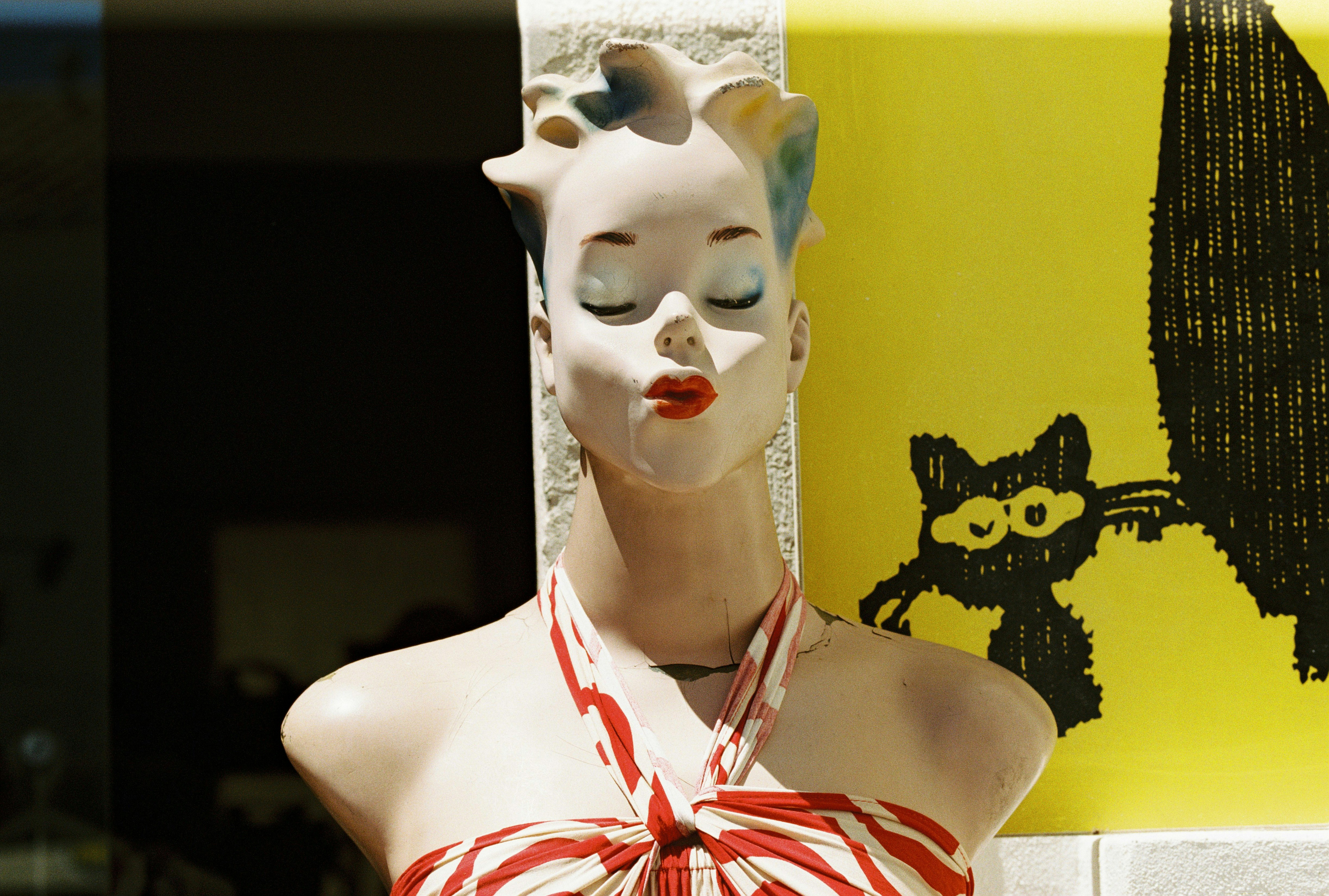 Mask of Mirth: A mannequin’s serene stare against a bold storefront mural
