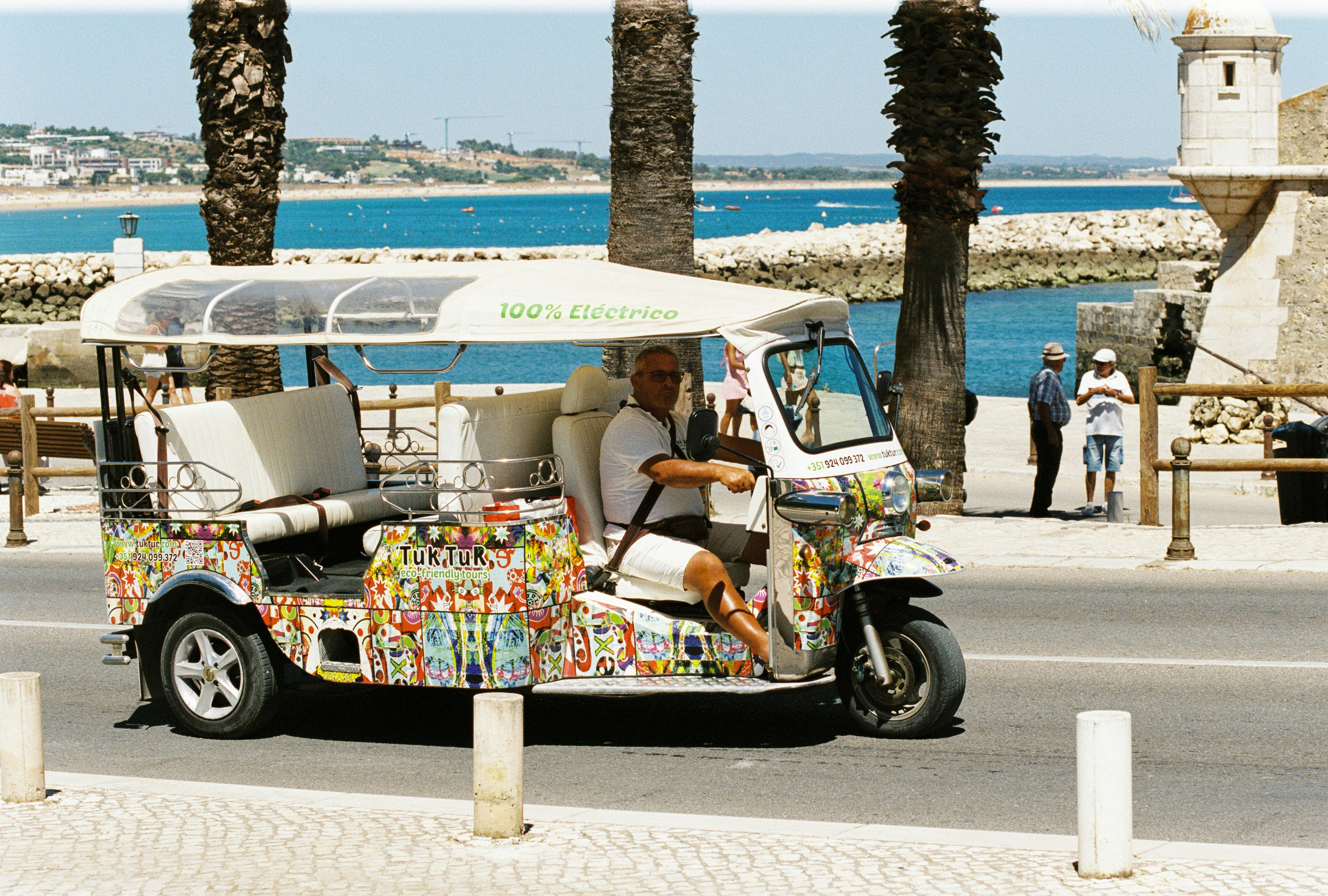 Colorful tuk-tuk by the sea: a sunny coastal scene with a driver