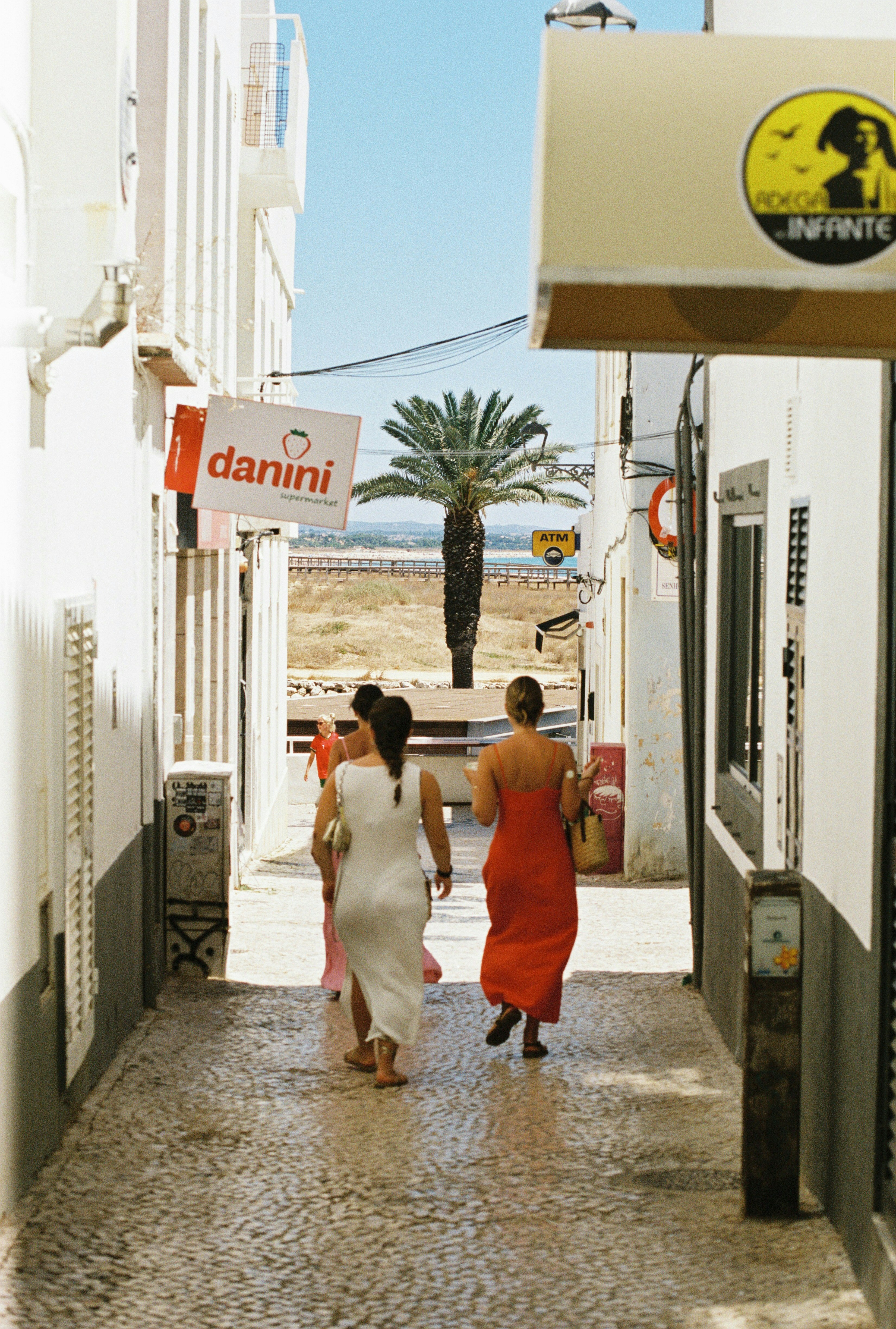 Sunlit Lane: Two Women in White and Orange Walk Toward a Distant Palm