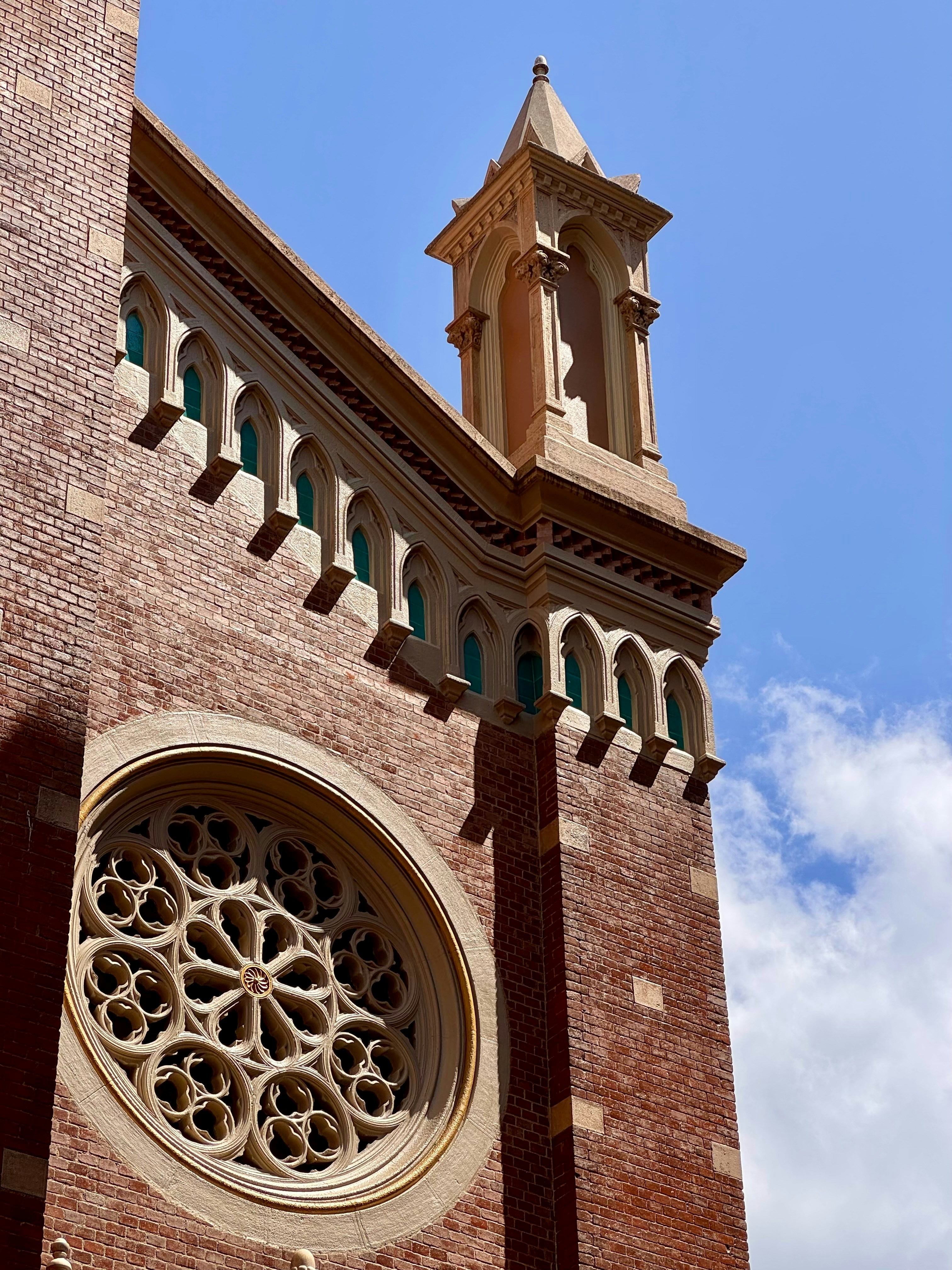 Brick clocktower facade with ornate circular window and arched openings against a blue sky.