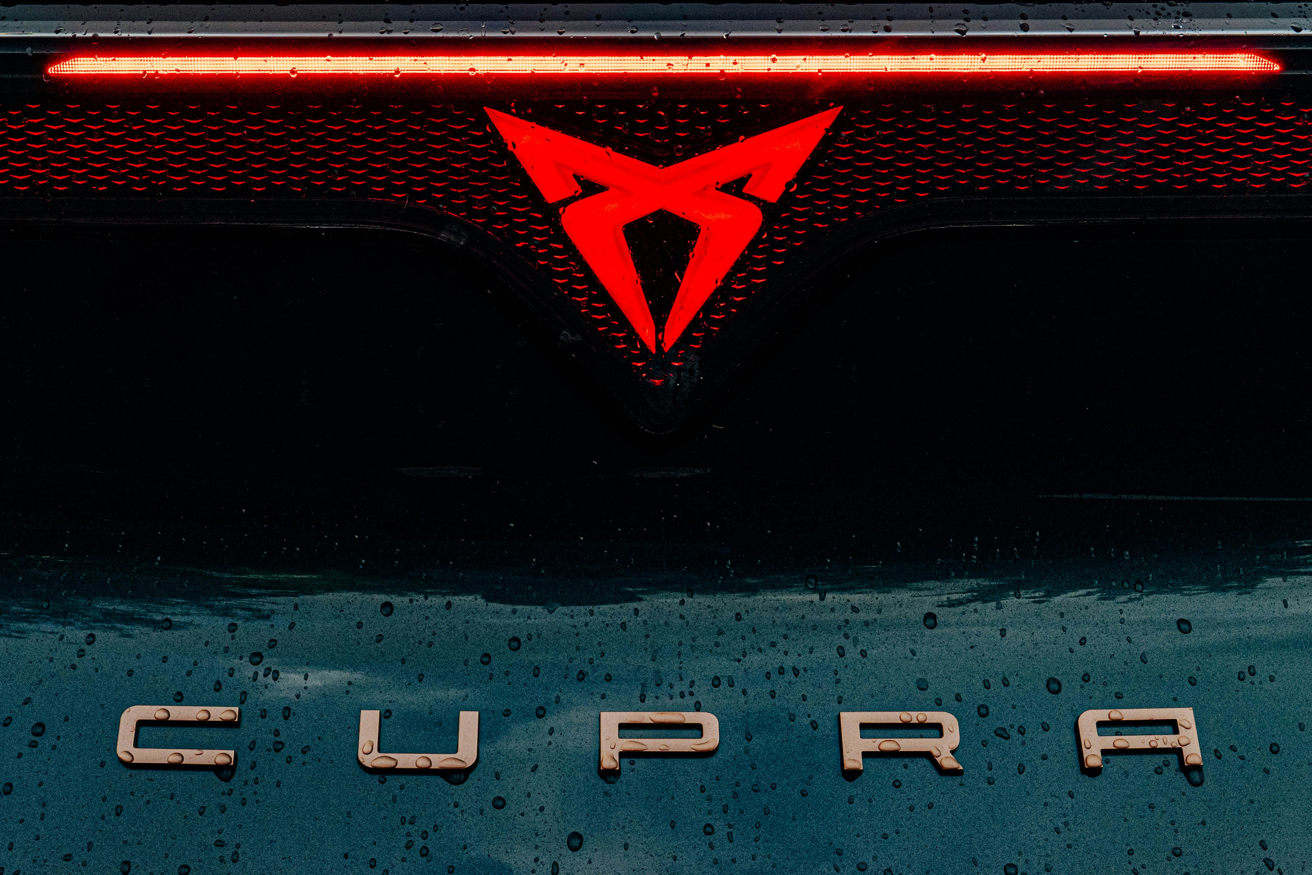 Red Emblem, Darkened Crest: The Cupra Emblem Framed by a Wet Backdrop