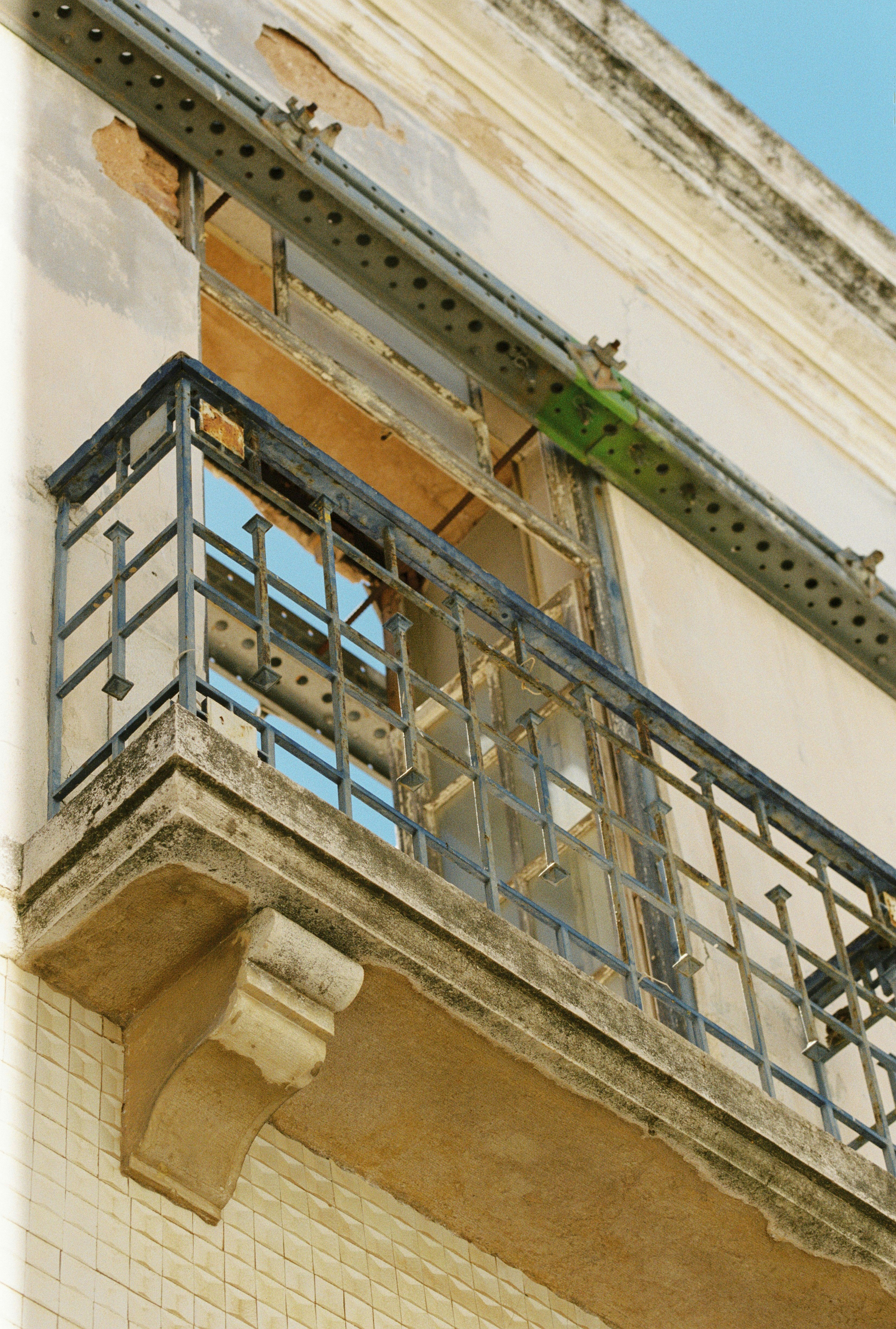 Weathered balcony railways: peeling paint and rusted metal above sunlit tiles
