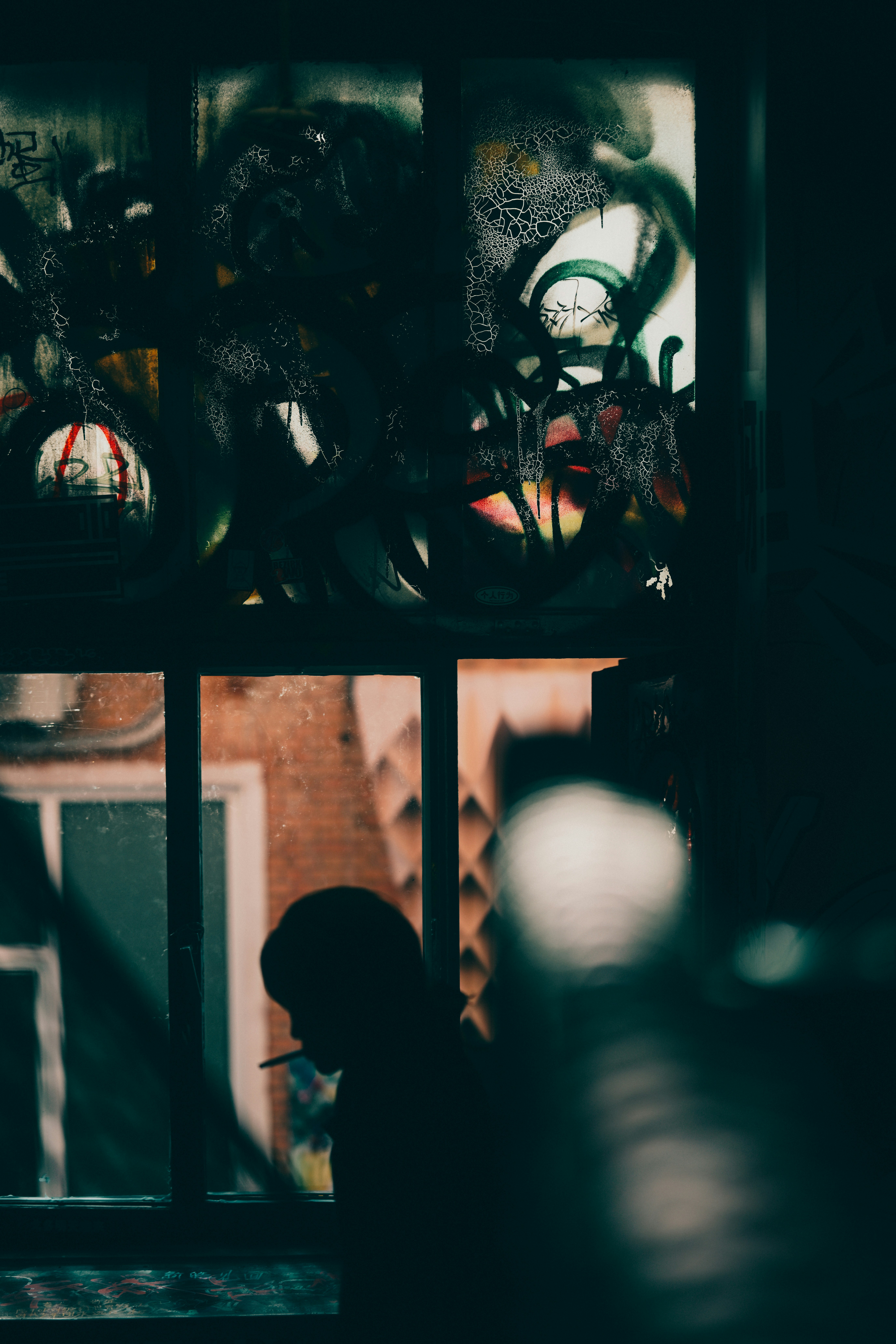 Silhouette through Graffiti Glass: A Quiet Moment in a Dim Corridor