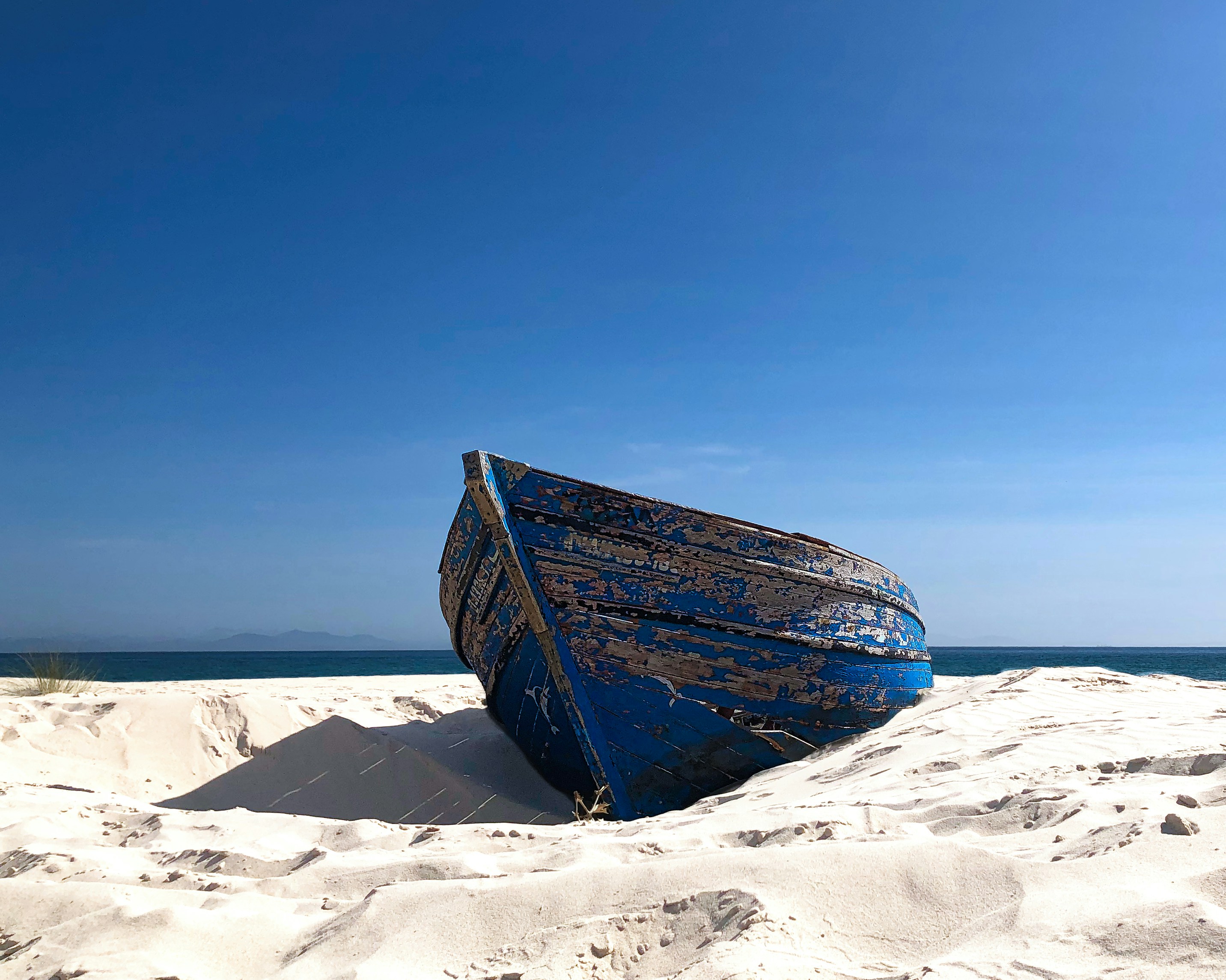 Blue Boat Half-Buried in White Sand, Under a Clear Coastal Sky