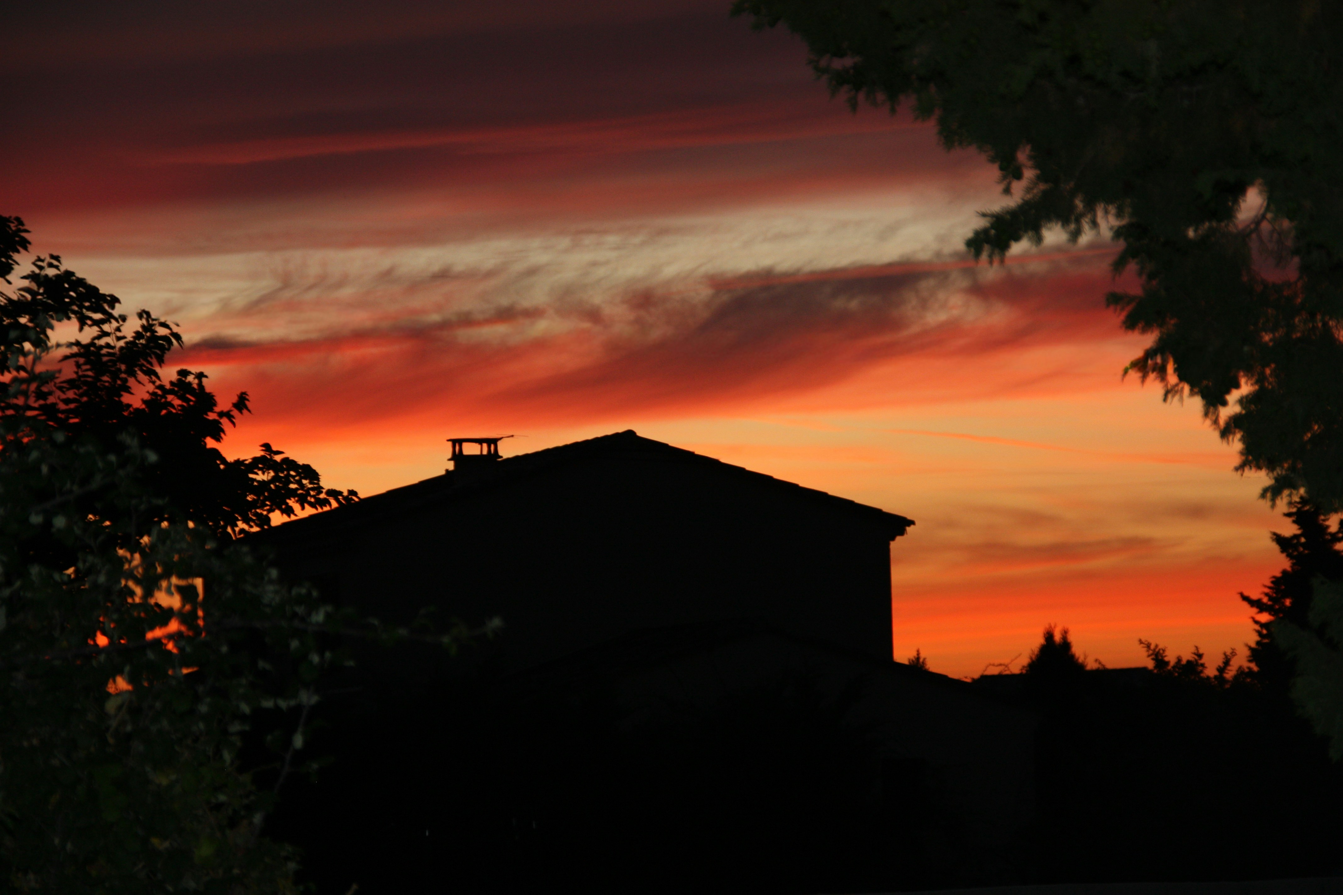 A house silhouette against a vibrant orange and red sky with tree branches