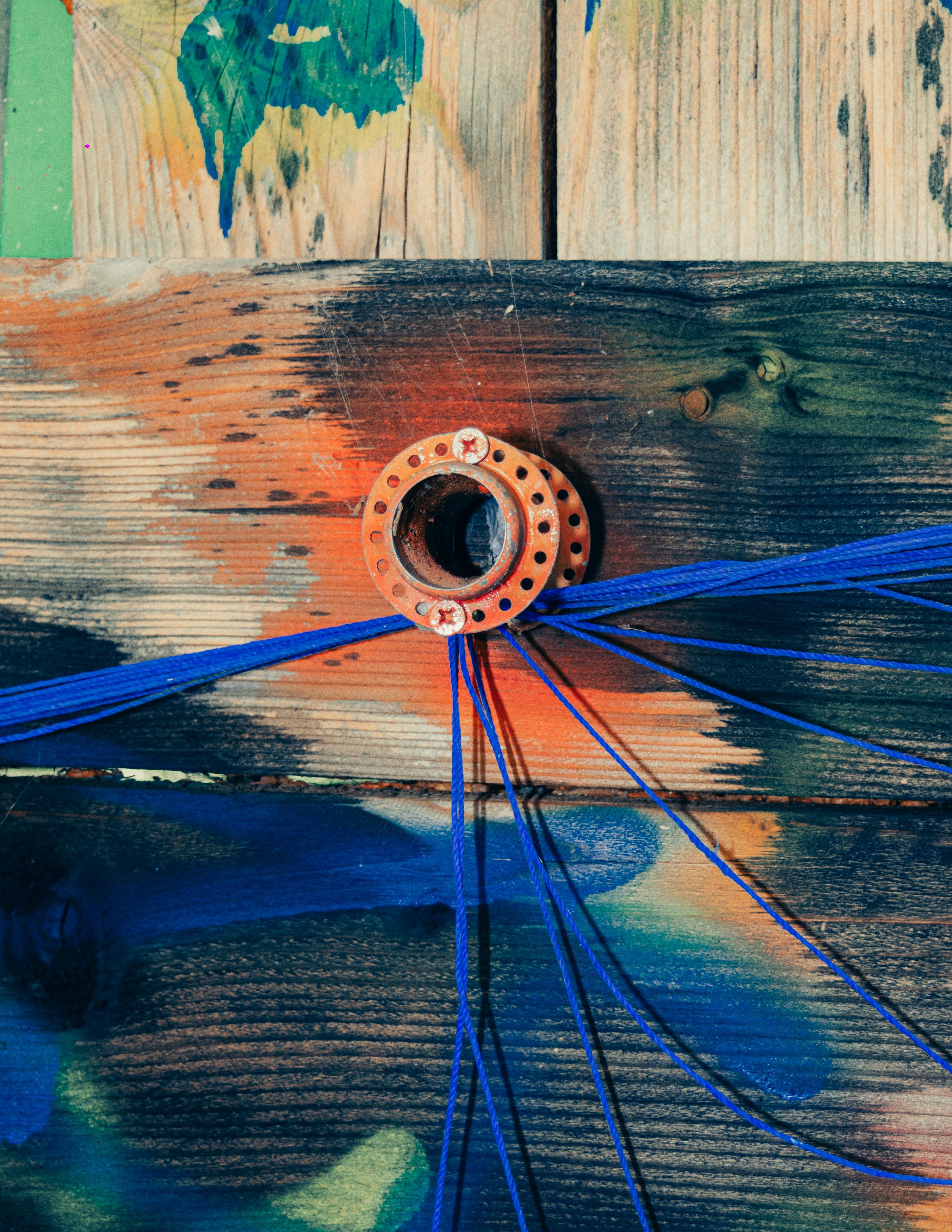 Blue Threads Converge at a Rusted Ring on Painted Wood