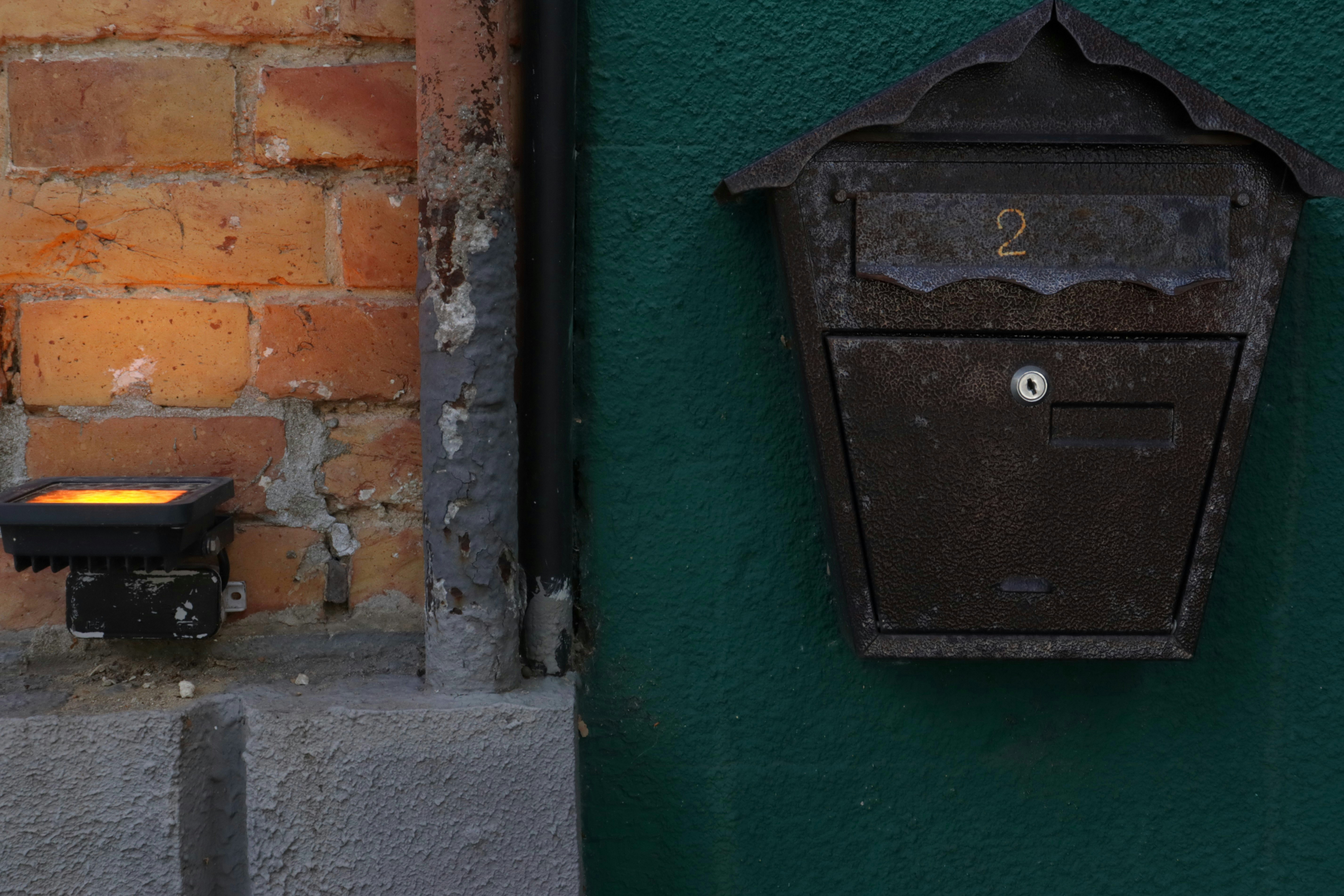 Left Wall Glow: A Weathered Mailbox by a Damp Green Facade