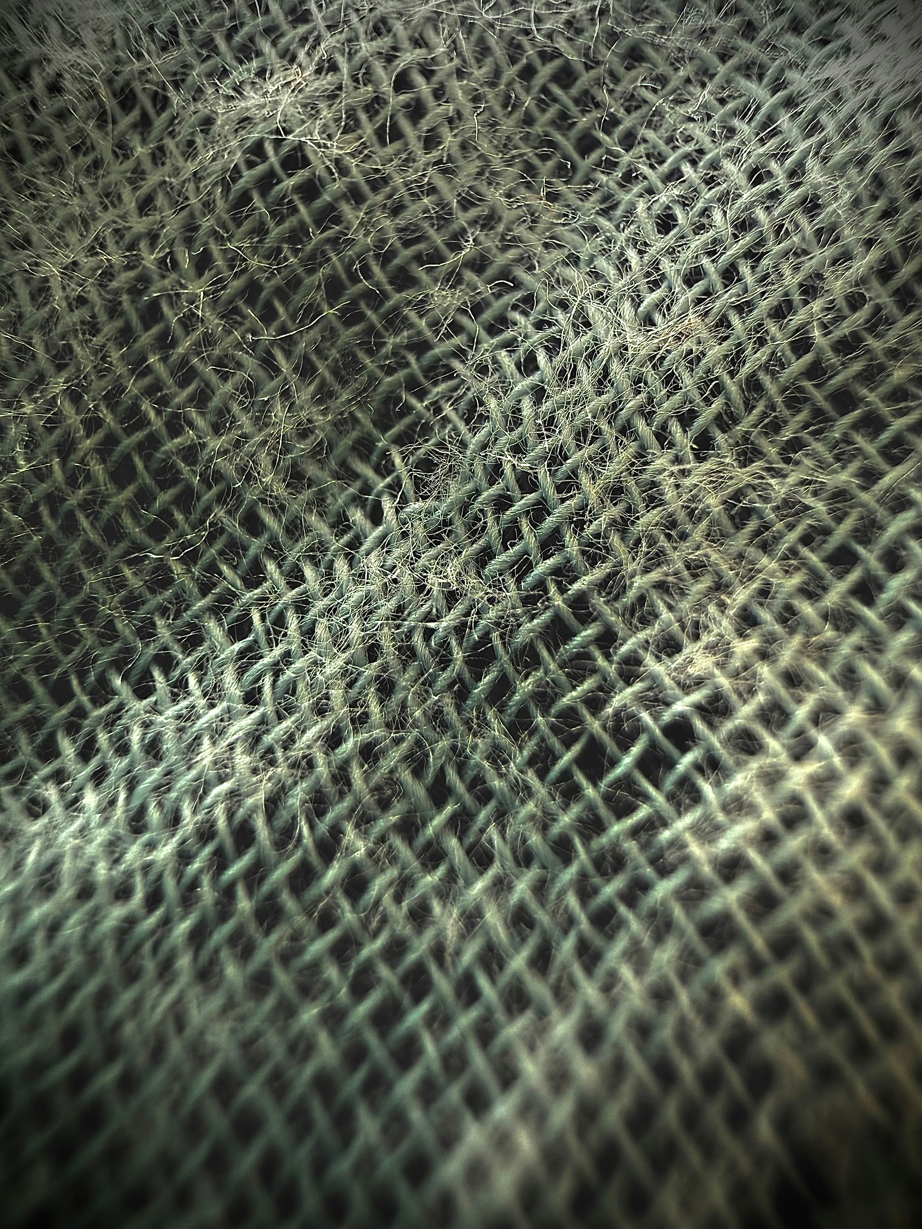 Close-up of green woven fabric with frayed fibers and a visible grid pattern