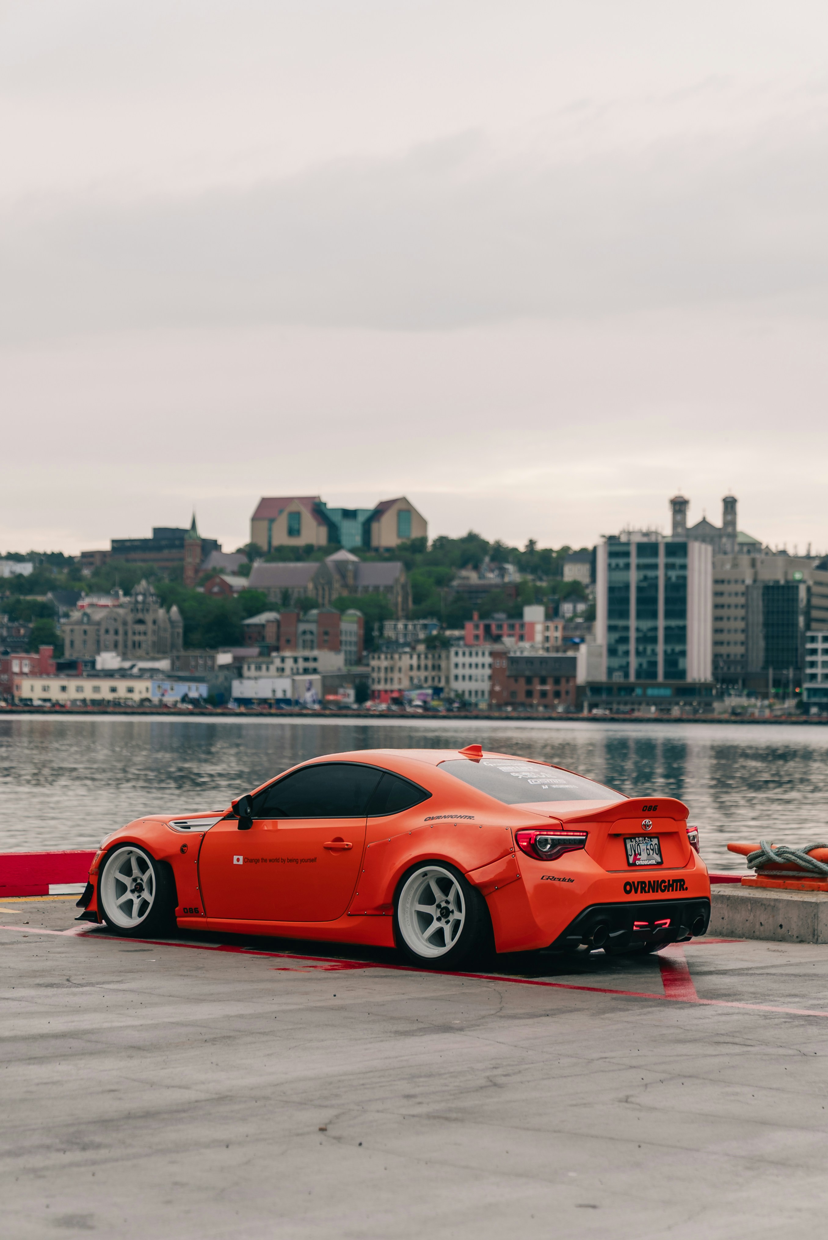 Red Gesture: A parked sports coupe by the water with cityscape backdrop
